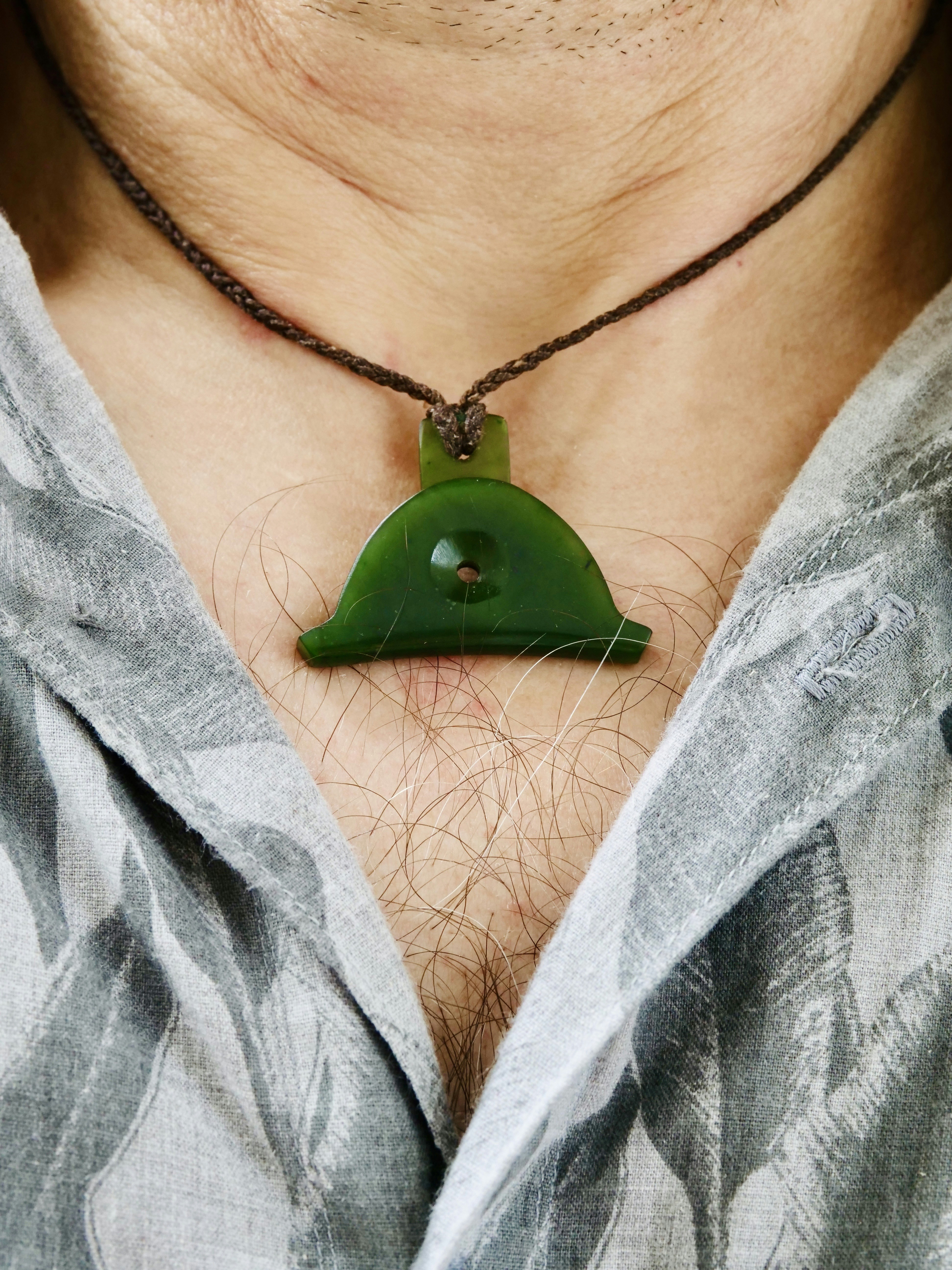 Green crescent pendant resting against exposed chest under open shirt