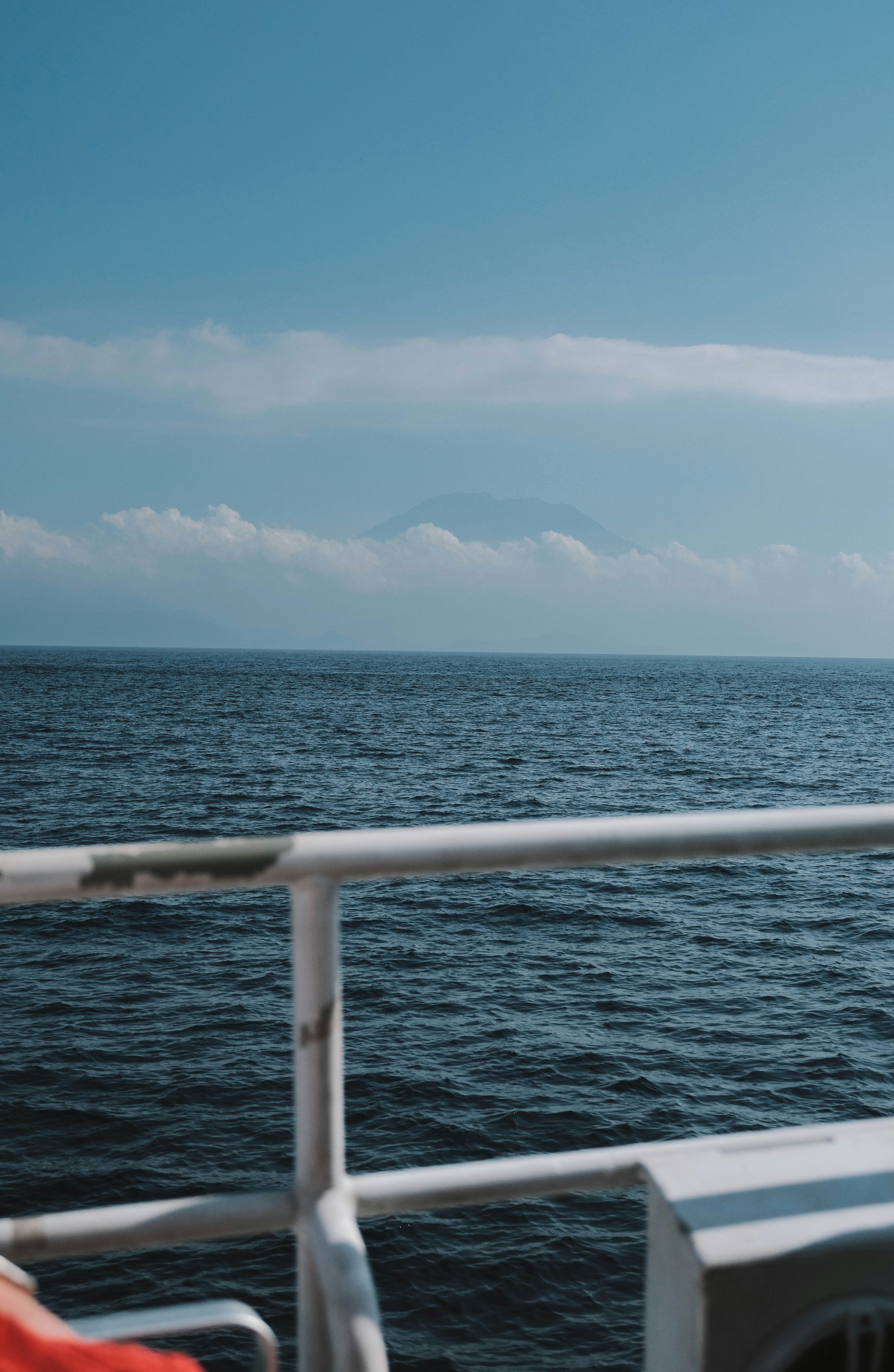 Calm sea vista from a railing on a vessel, with distant horizon and subtle clouds. A clean ocean expanse foregrounds the tranquil mood of travel at sea.