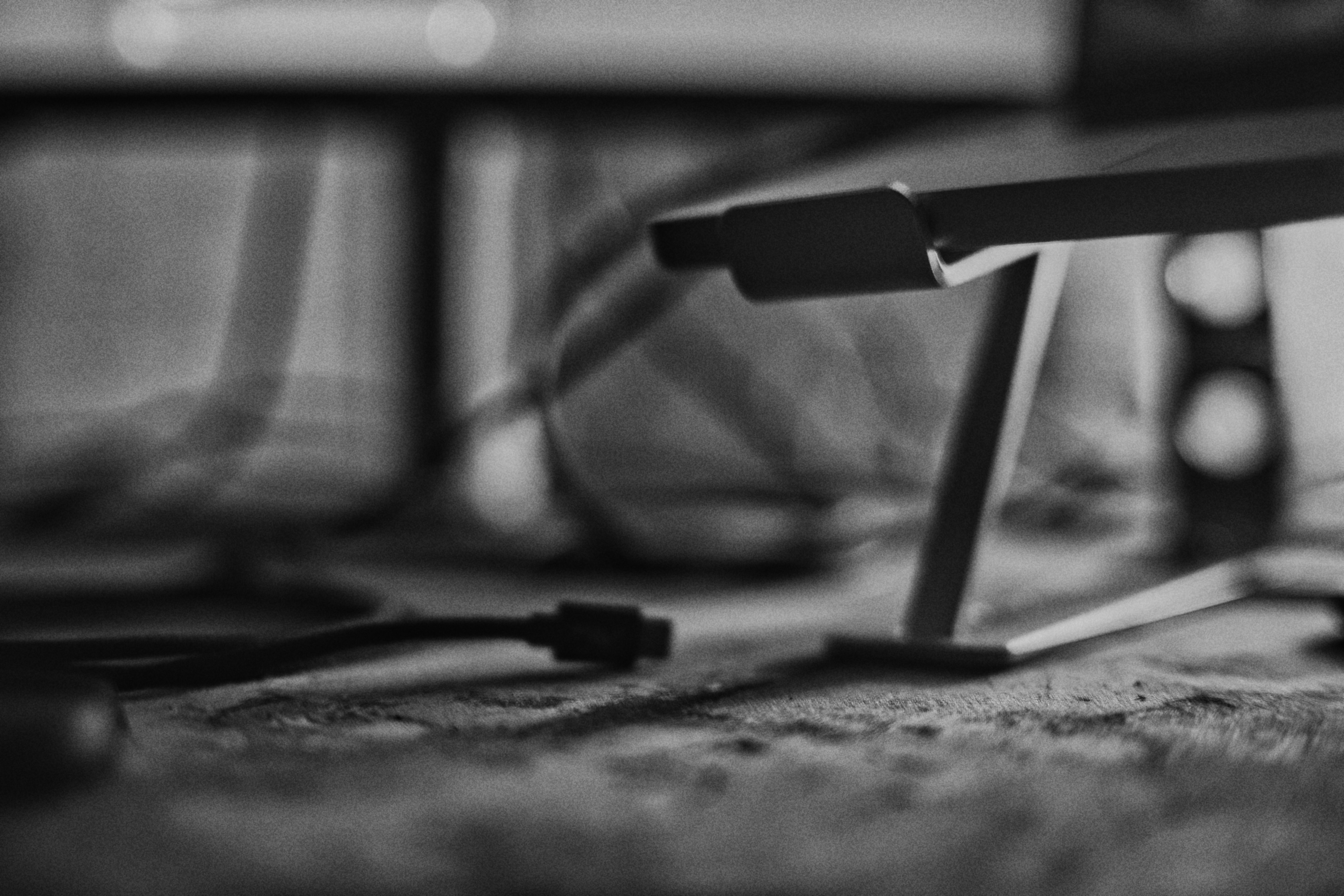 Monochrome close-up of a small desk stand and cables on a textured surface, emphasizing engineering silhouettes and tactile materials. This is a photographic study rather than an illustration or logo.