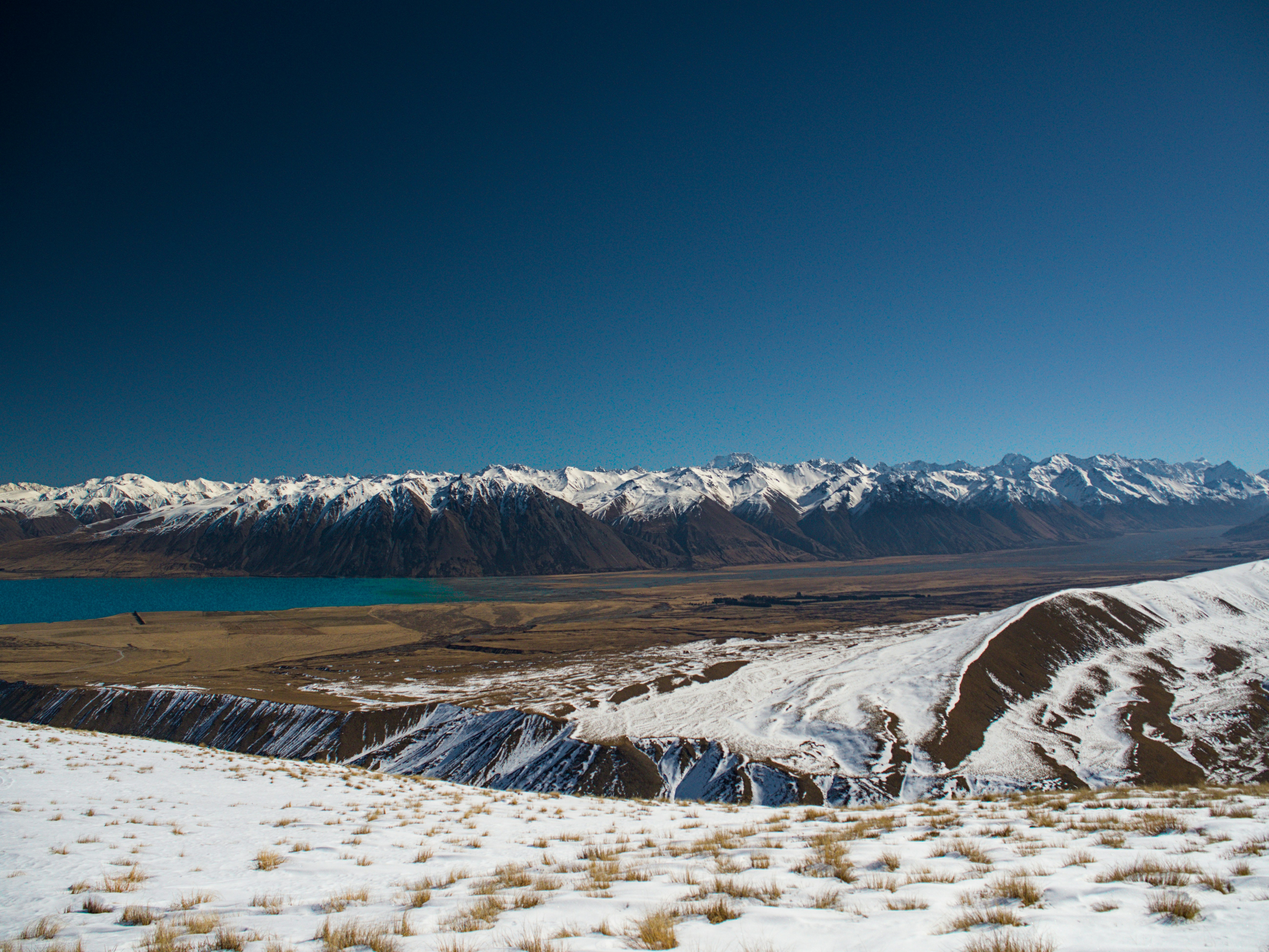 Snow-kissed ridge over a distant turquoise lake under a cobalt sky