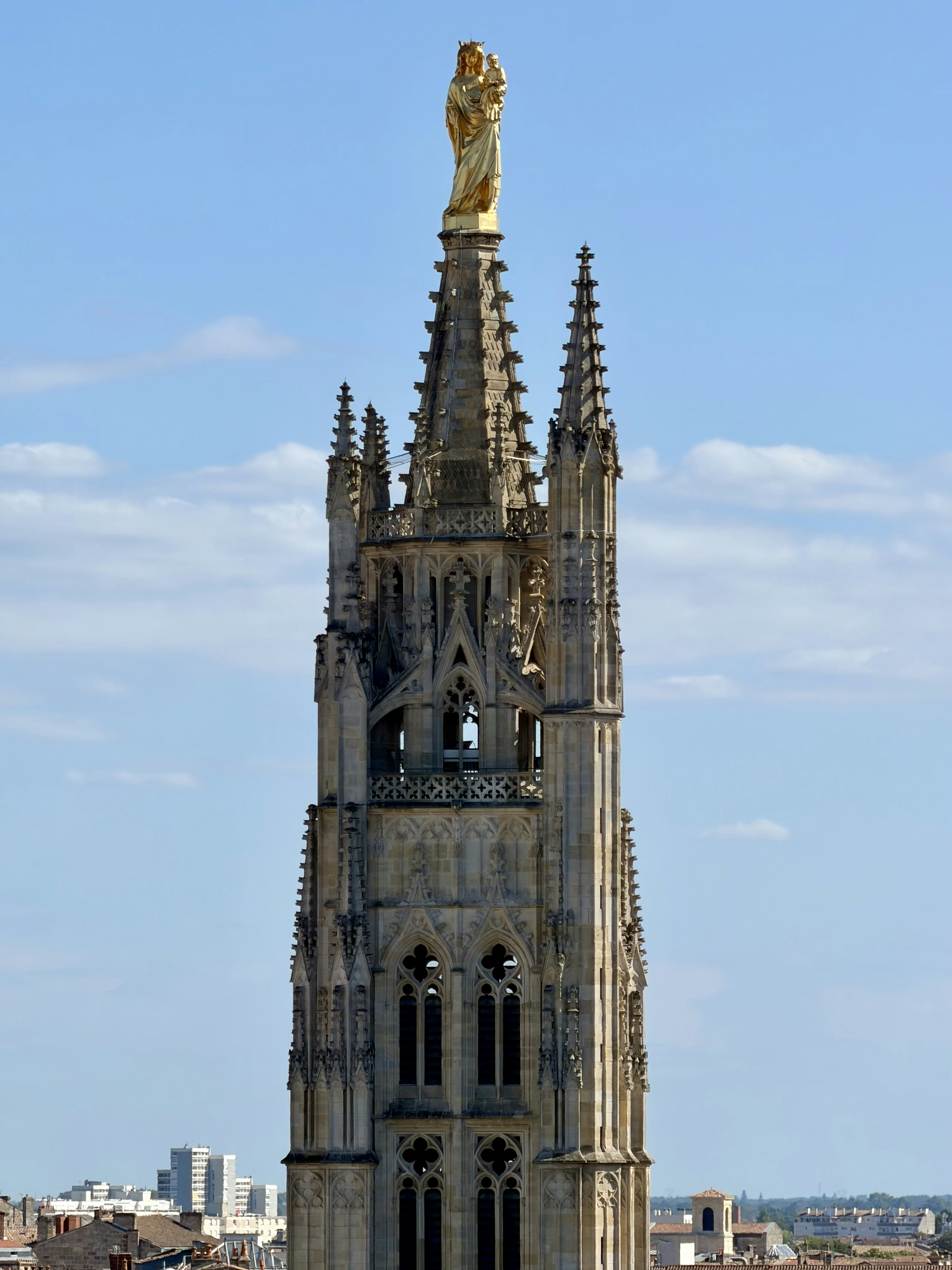 Golden statue atop a Gothic spire rises above a cityscape