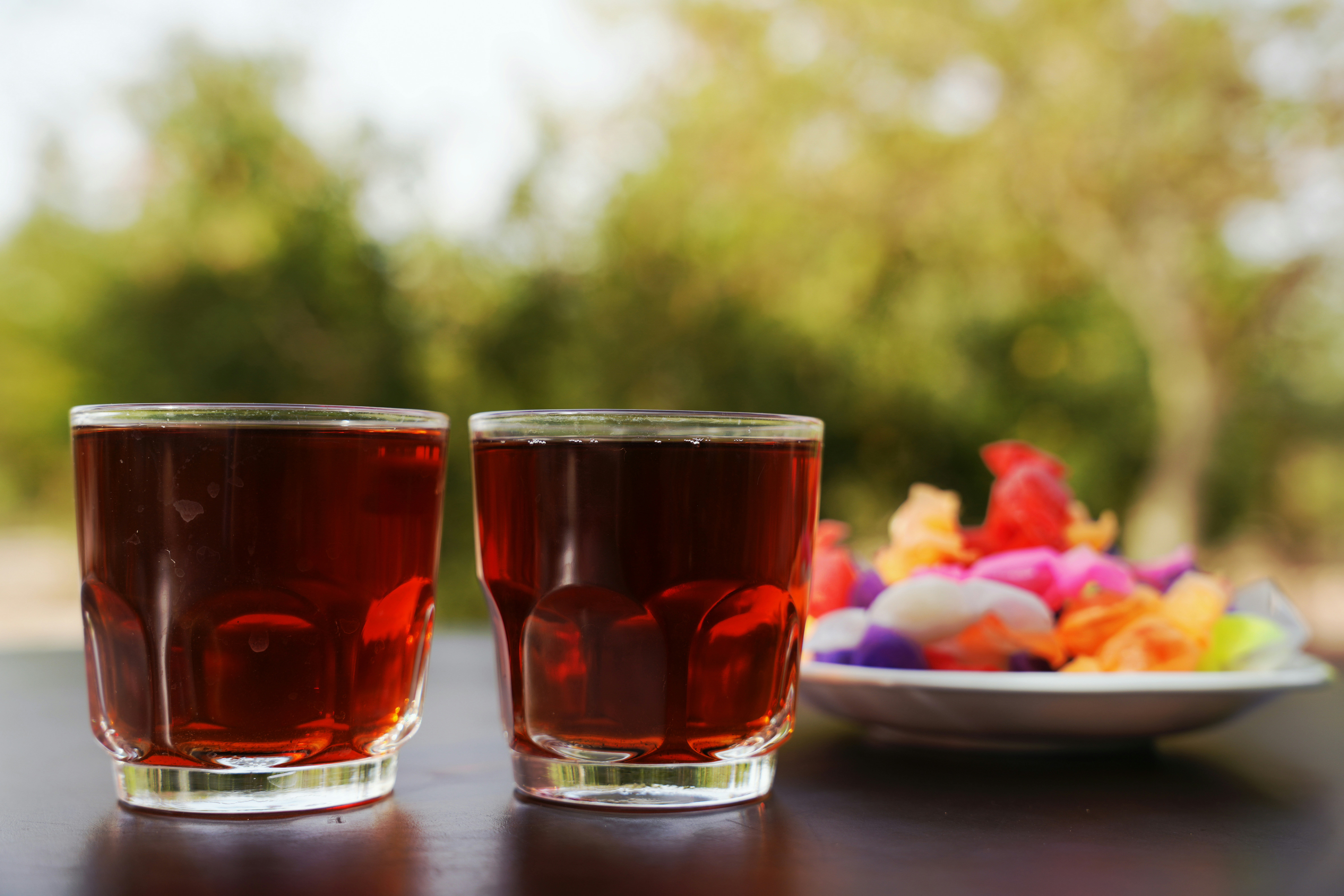 Twin Glimmers: Two Burgundy Glasses foreground with a colorful plate in soft focus