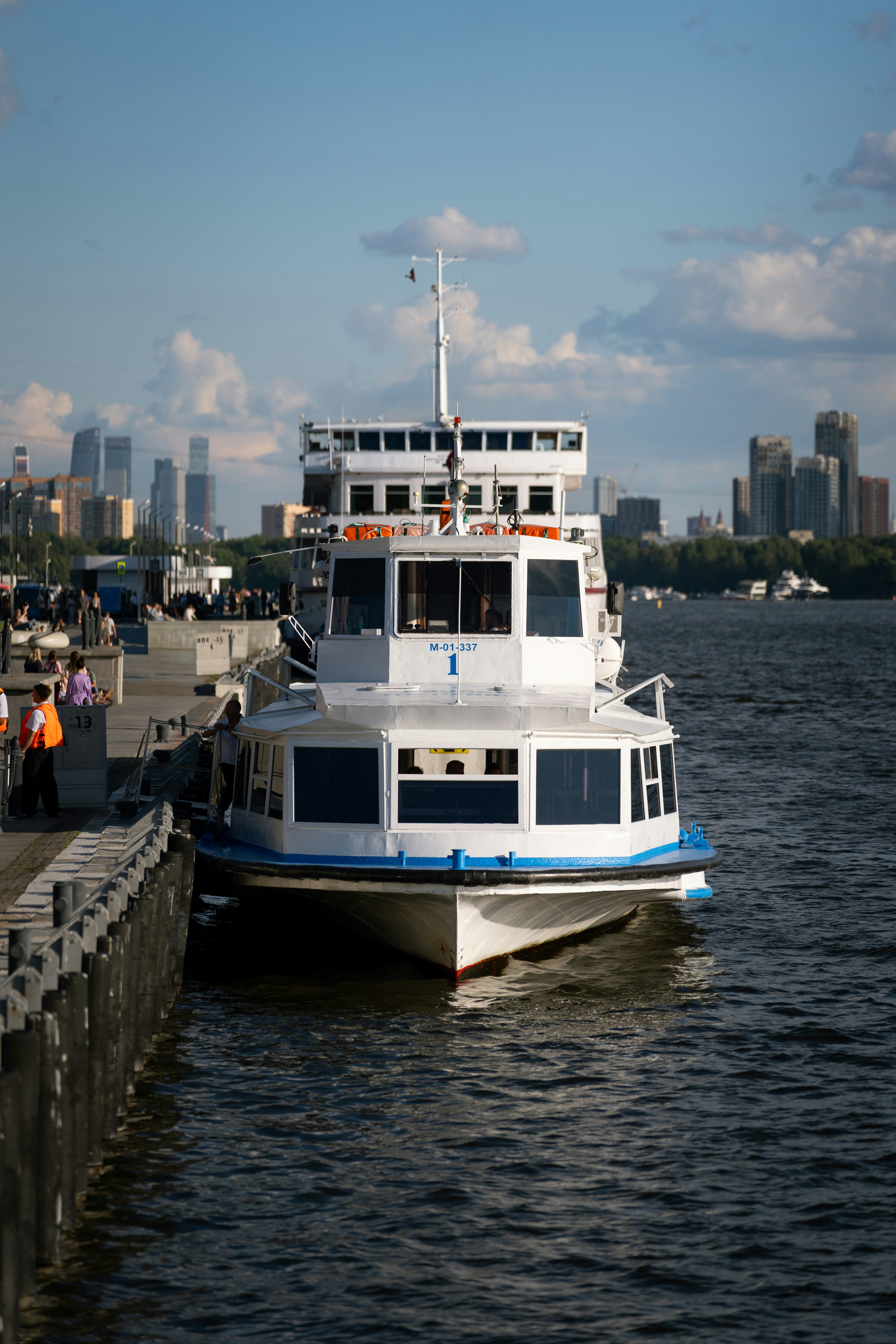 White passenger ferry at a riverside dock with city skyline backdrop