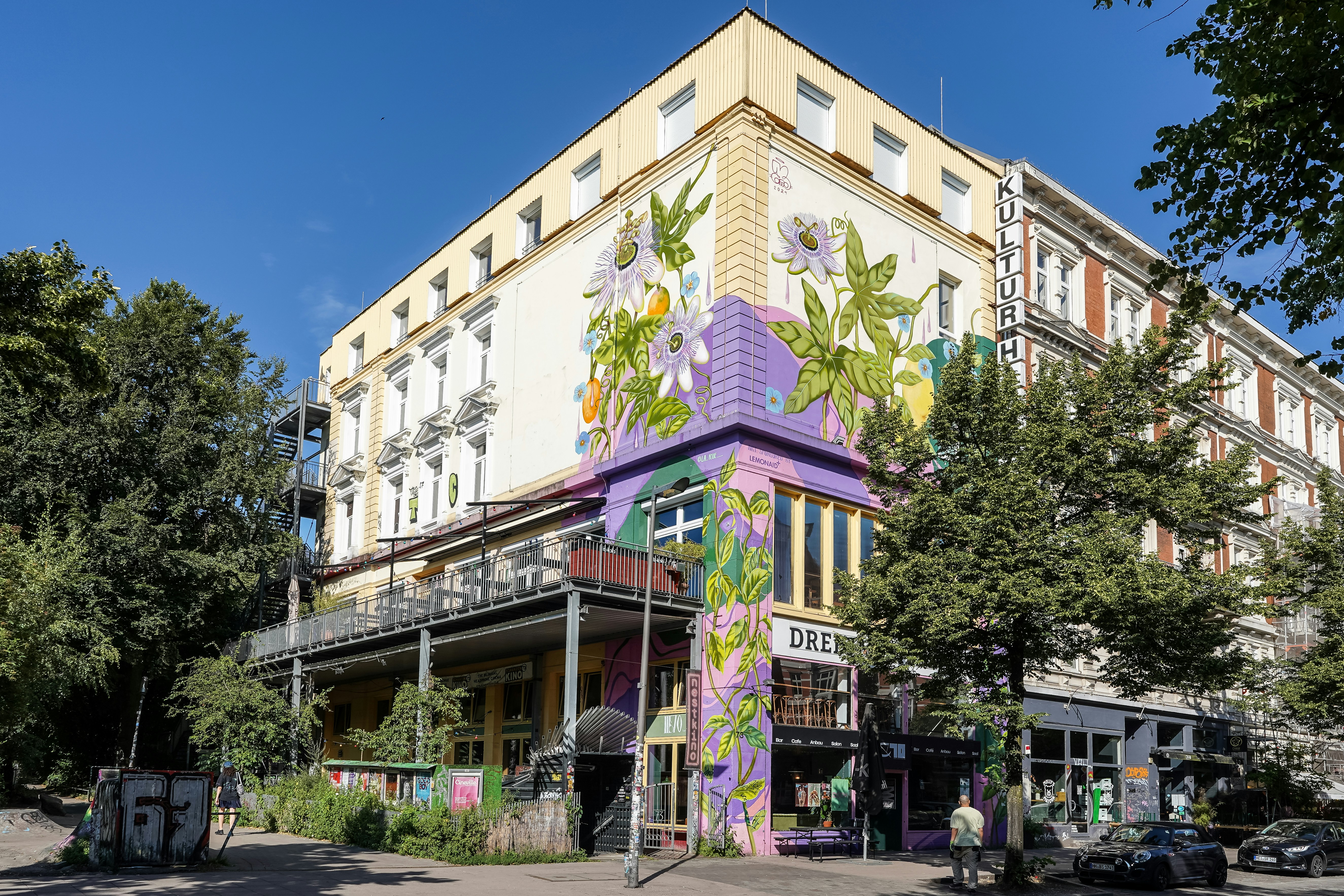 Vibrant mural-wrapped corner storefront anchors a sunlit urban block