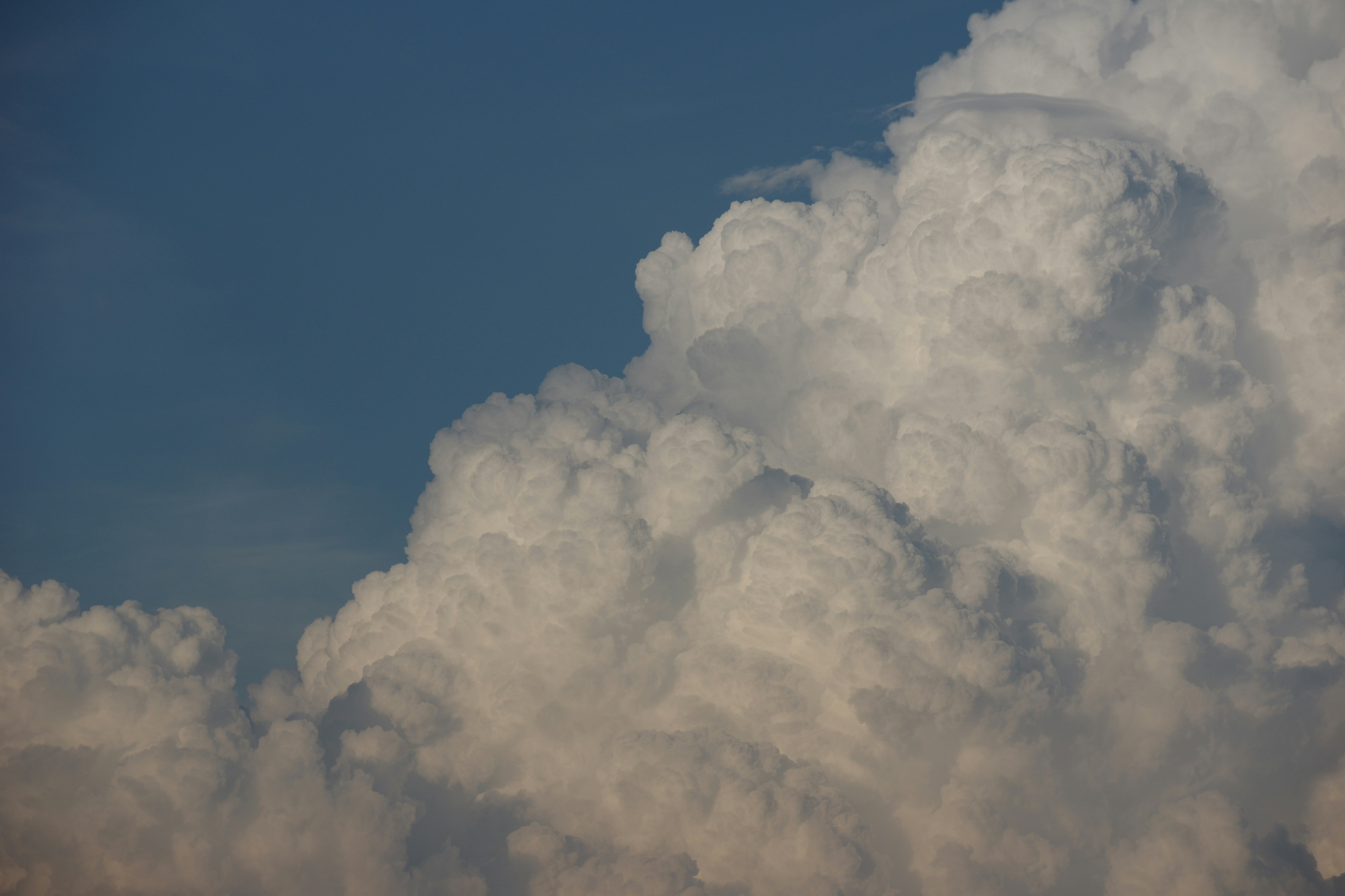 Massive cumulus clouds rise against a clear sky, forming a soft, sunlit sculpted mass that dominates the frame and suggests calm atmospheric depth.