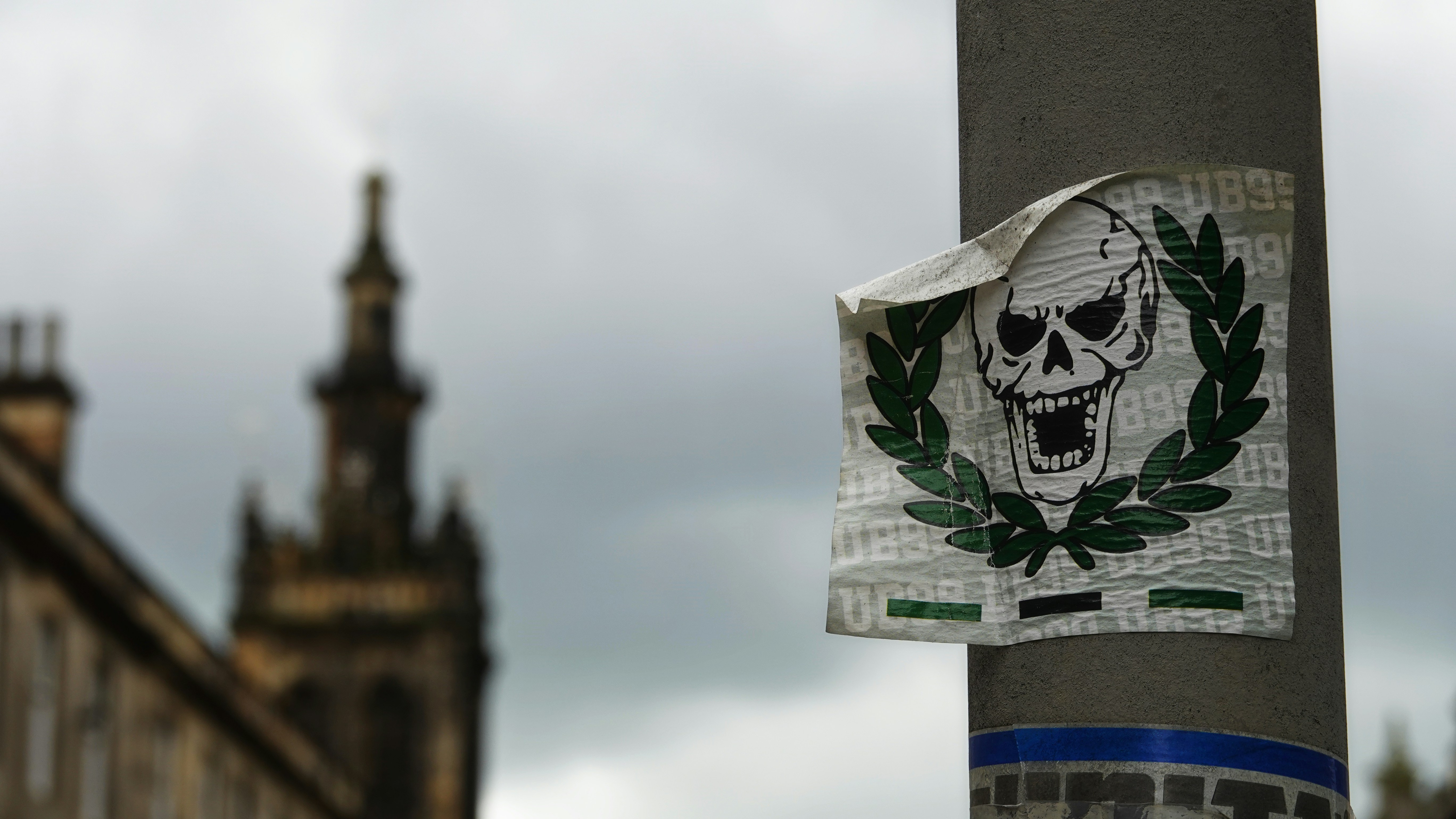 Stickered Beacon: Skull Laurel on a Weathered City Pole