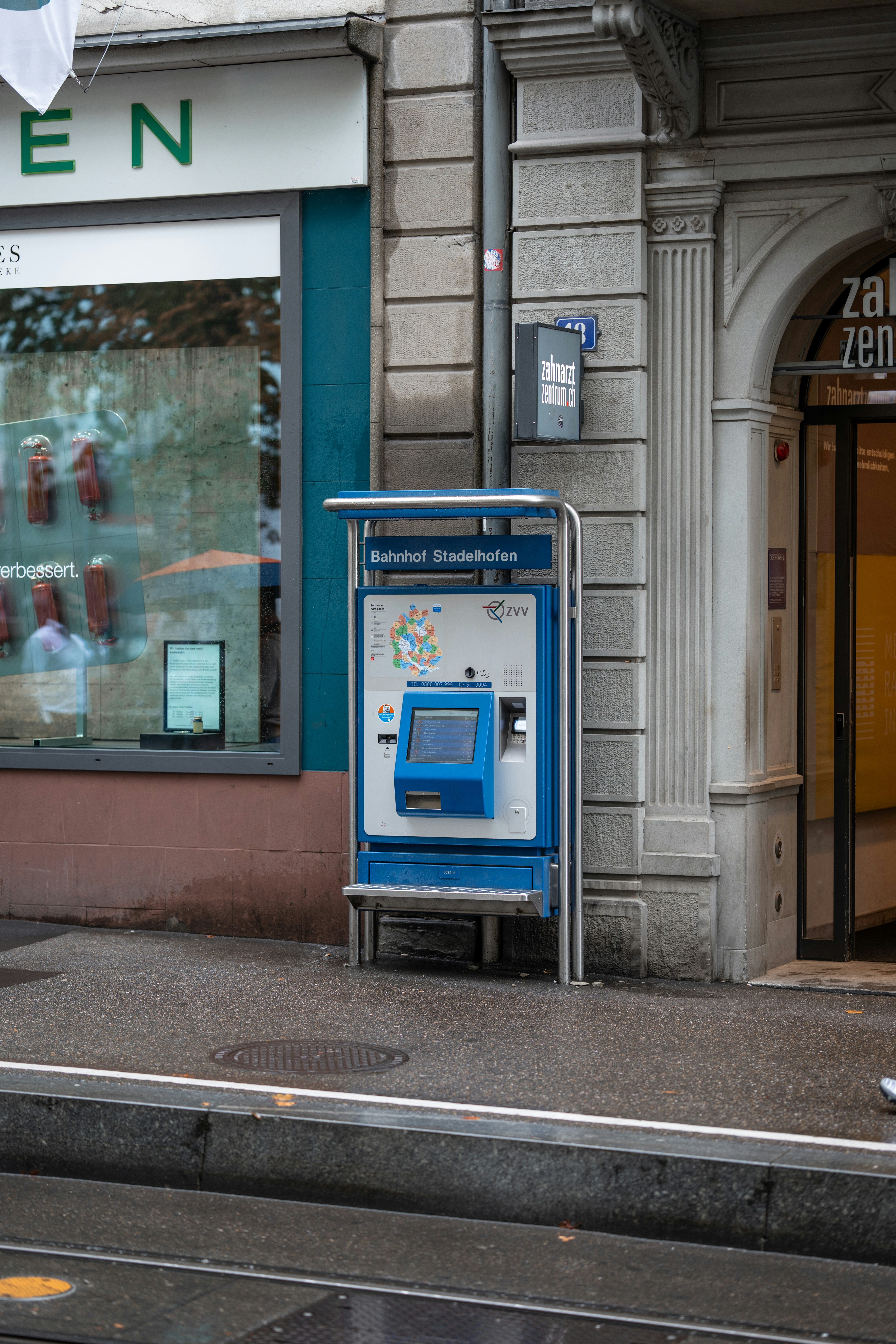Blue kiosk by a historic facade on a bustling street