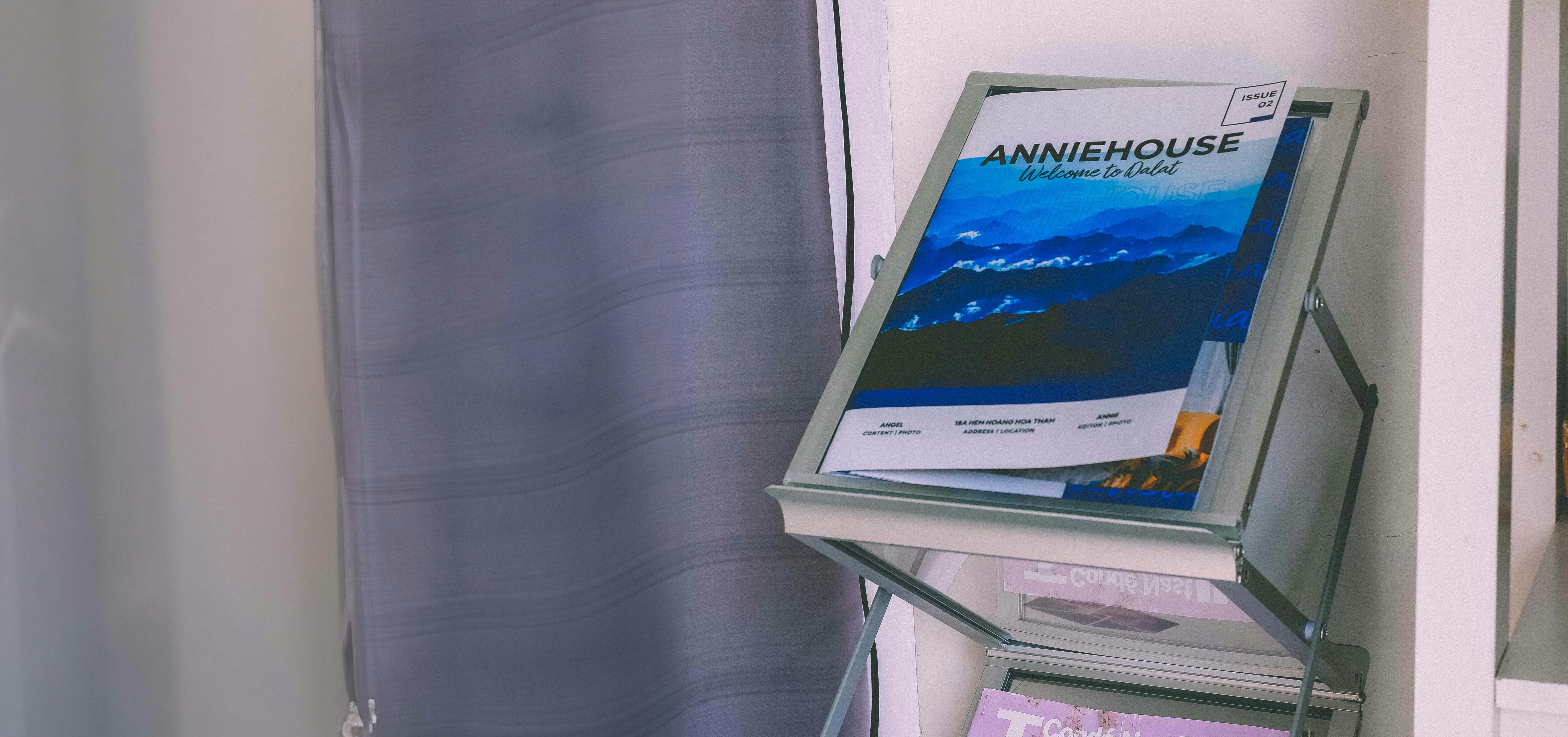 A magazine titled Anniehouse on a metal display stand beside a grey curtain