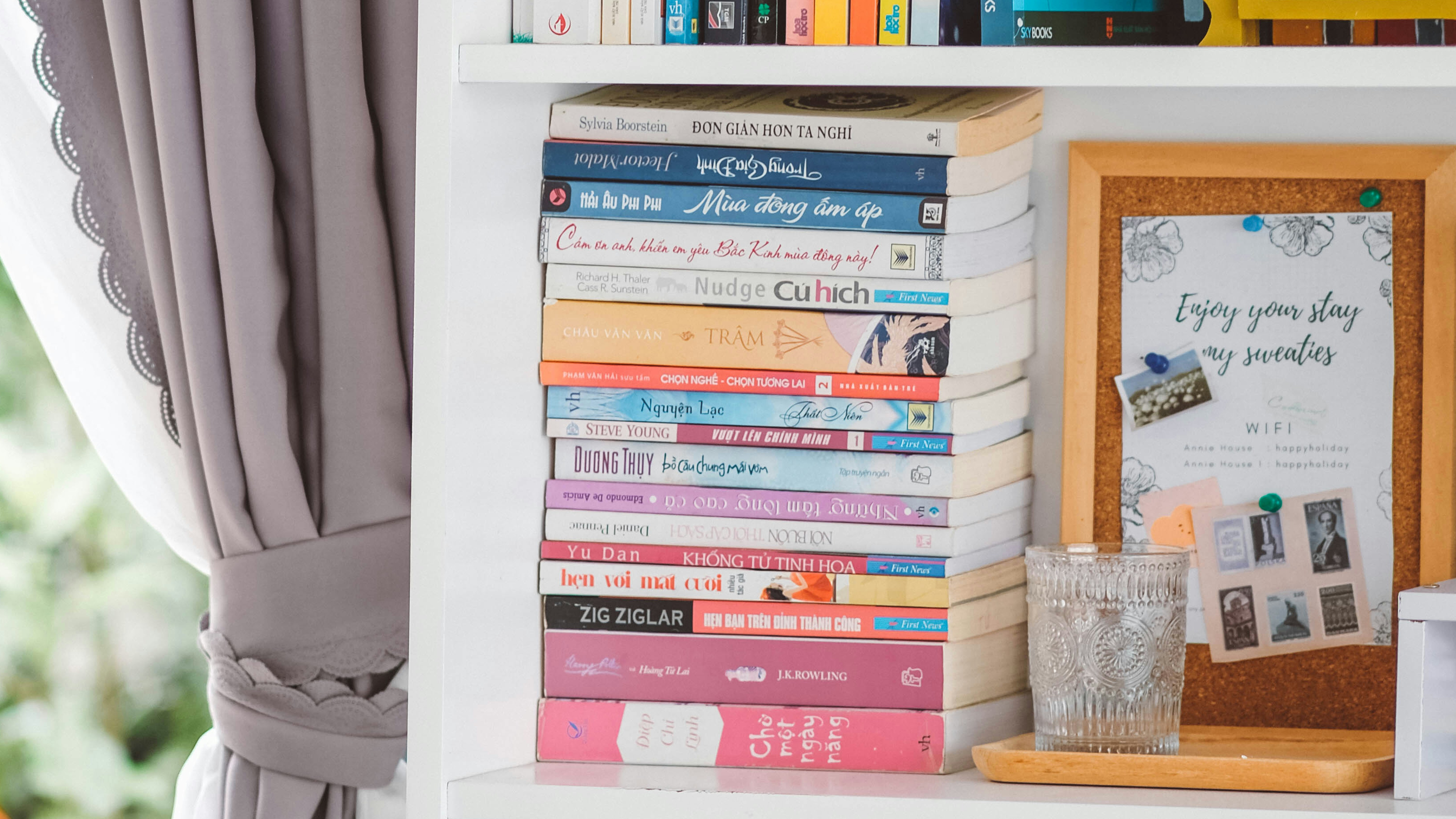 Colorful stack of books on a white bookshelf with a framed note
