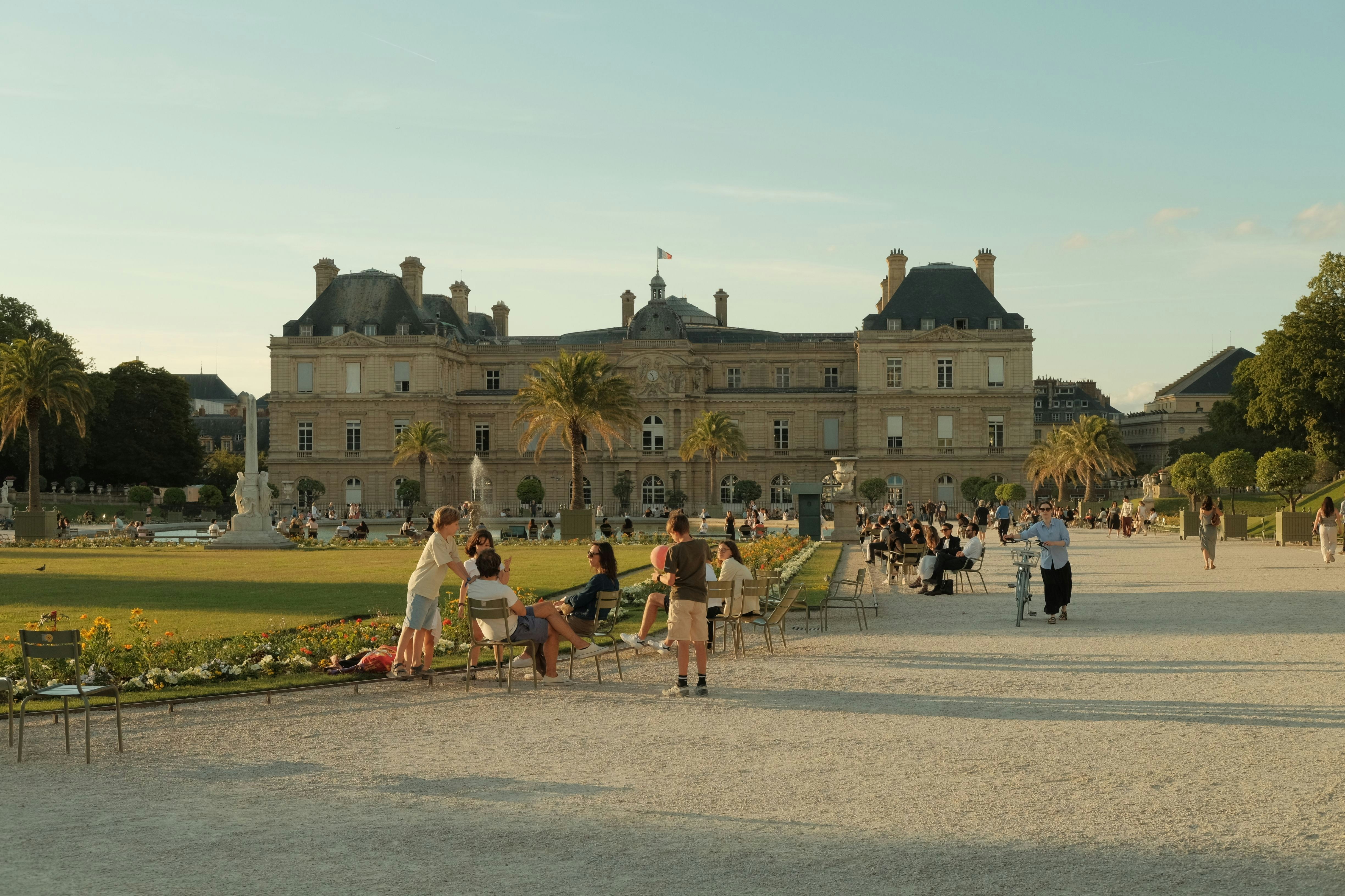 Guests at a sunlit park in front of a grand palace