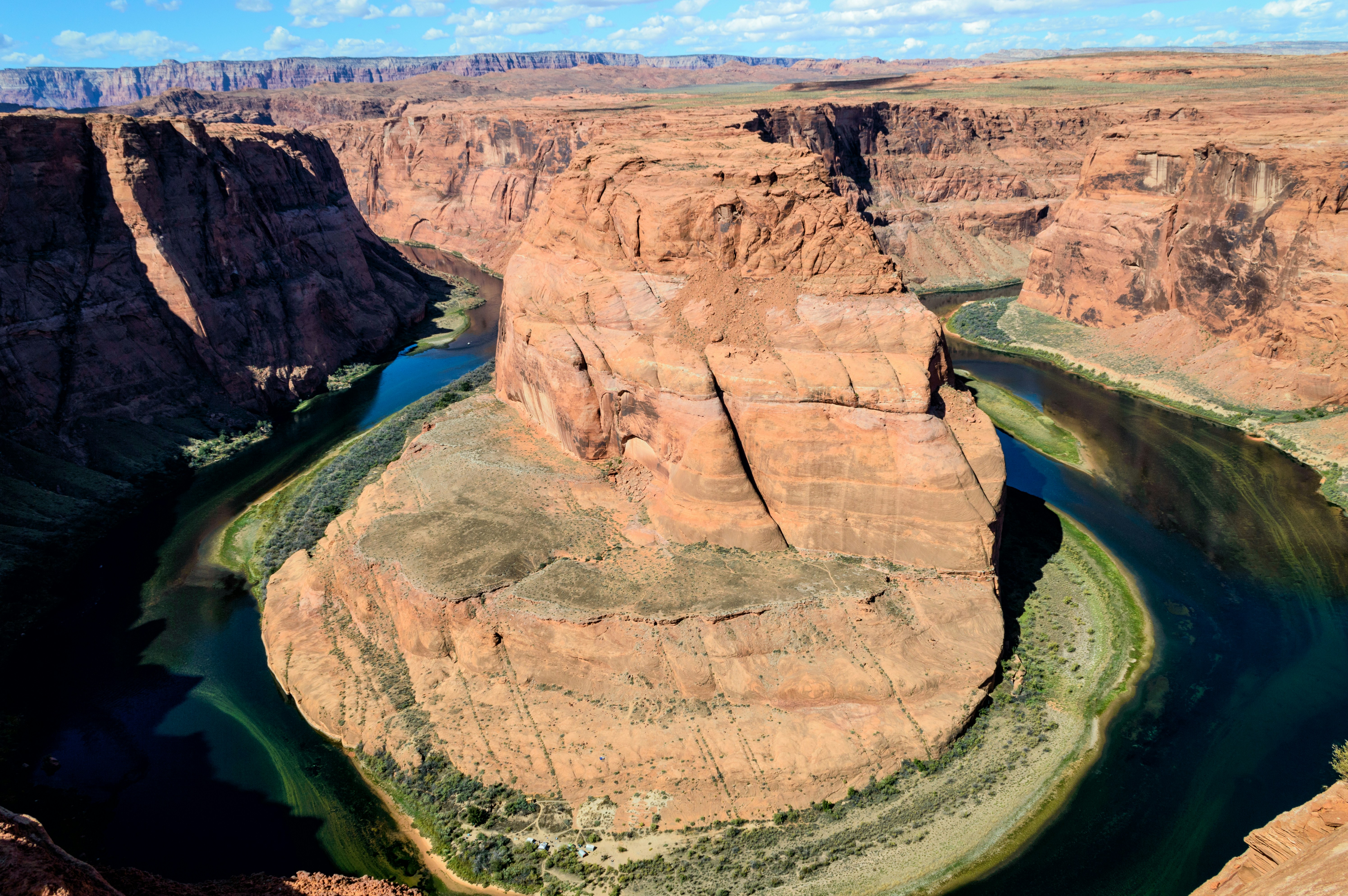 A towering sandstone formation curves the green river in a dramatic canyon, captured from above at midday, highlighting the sculpted walls and sinuous waterway.