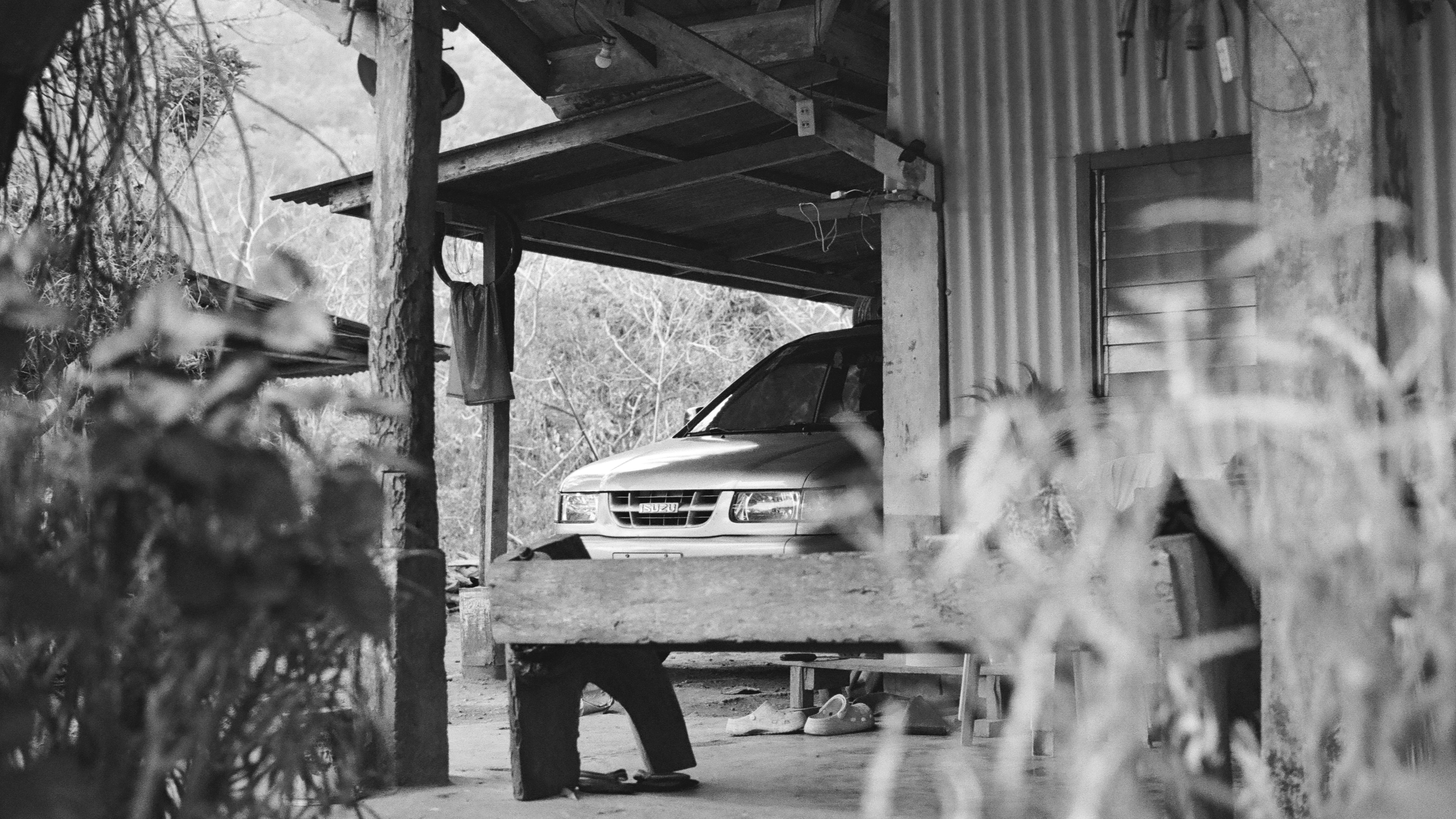 A car parked under a rustic wooden shelter beside a corrugated metal wall