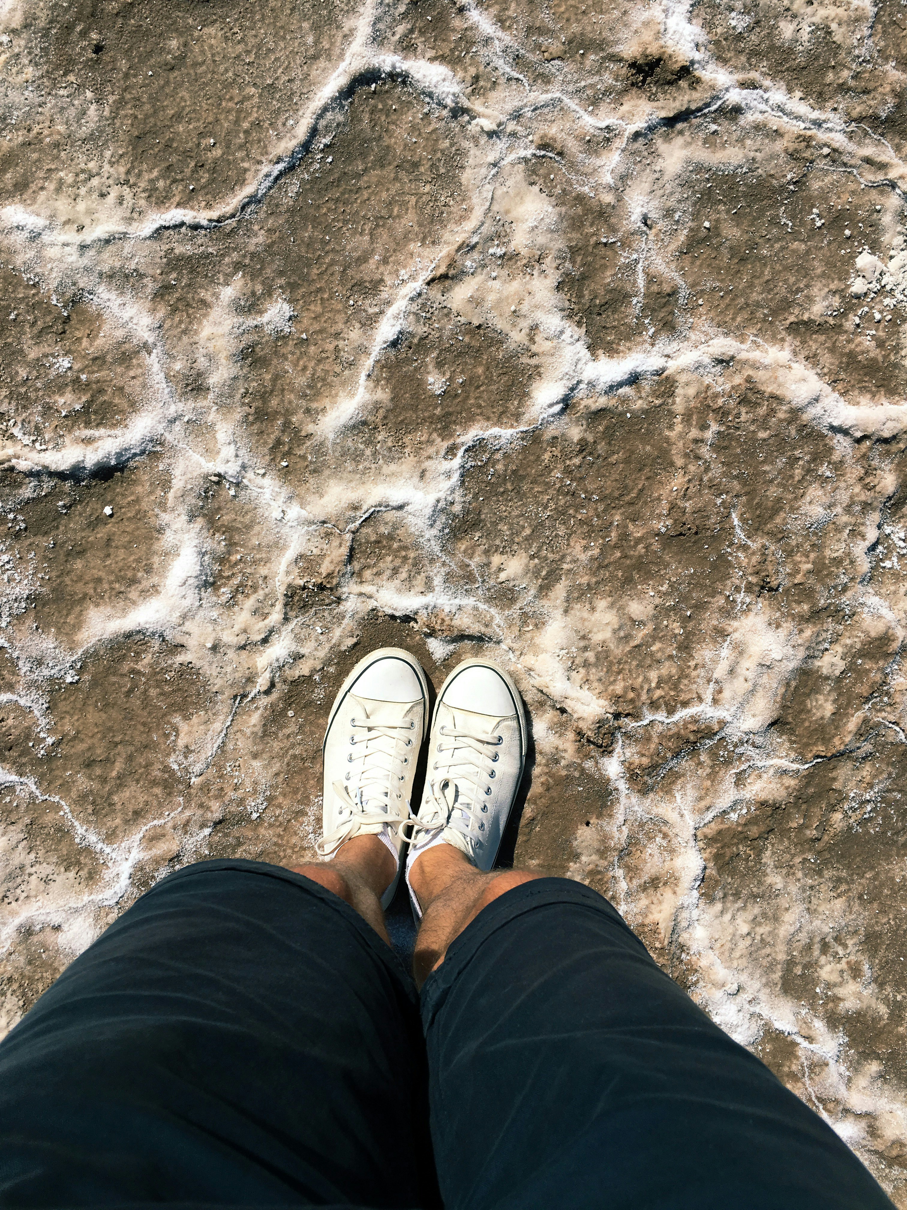 Two white sneakers seen from above stand on a rough stone surface with light veins; a casual scene highlighting texture and footwear.