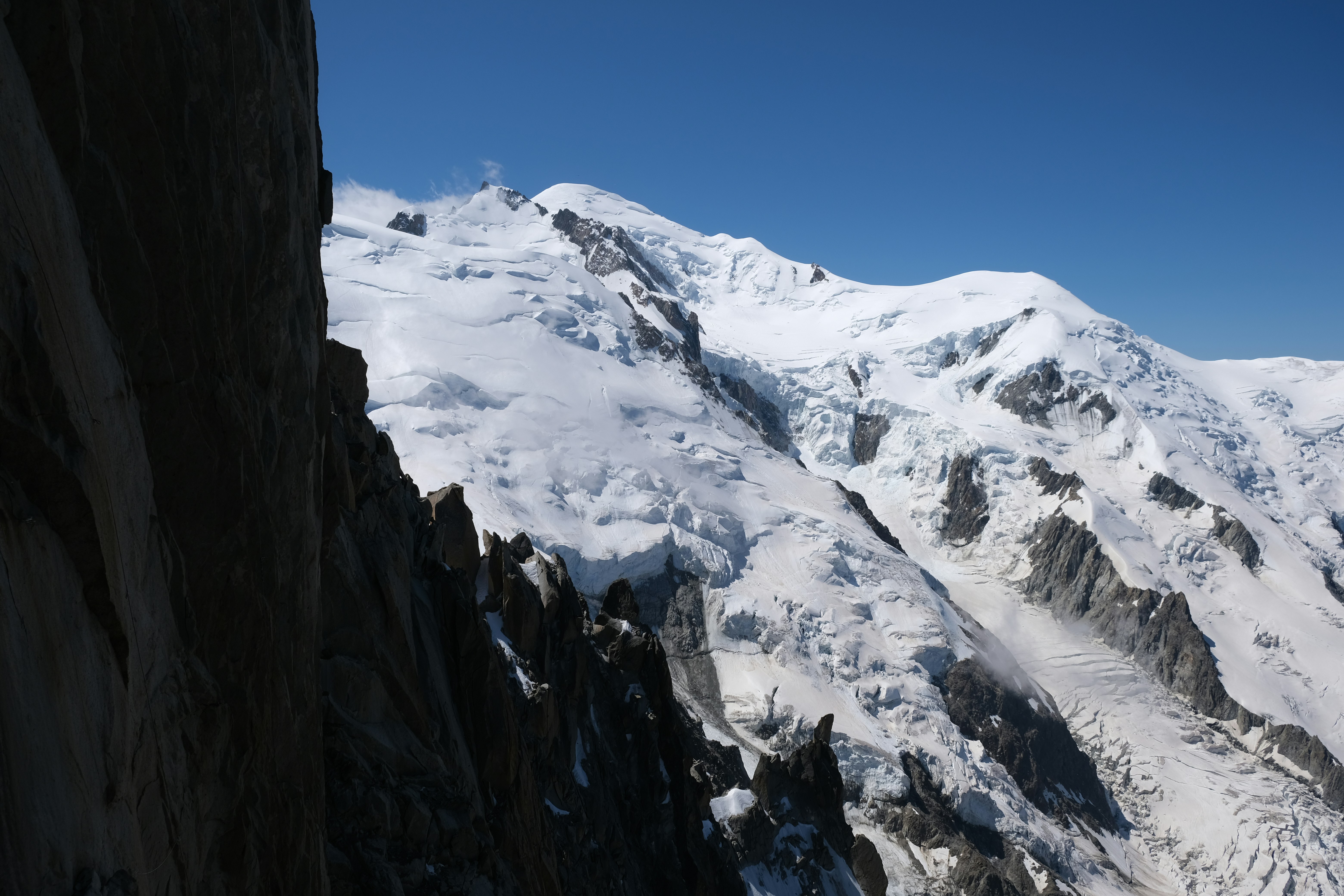Snow-covered alpine ridge with dark rock faces under a clear blue sky, capturing expansive high-altitude terrain.