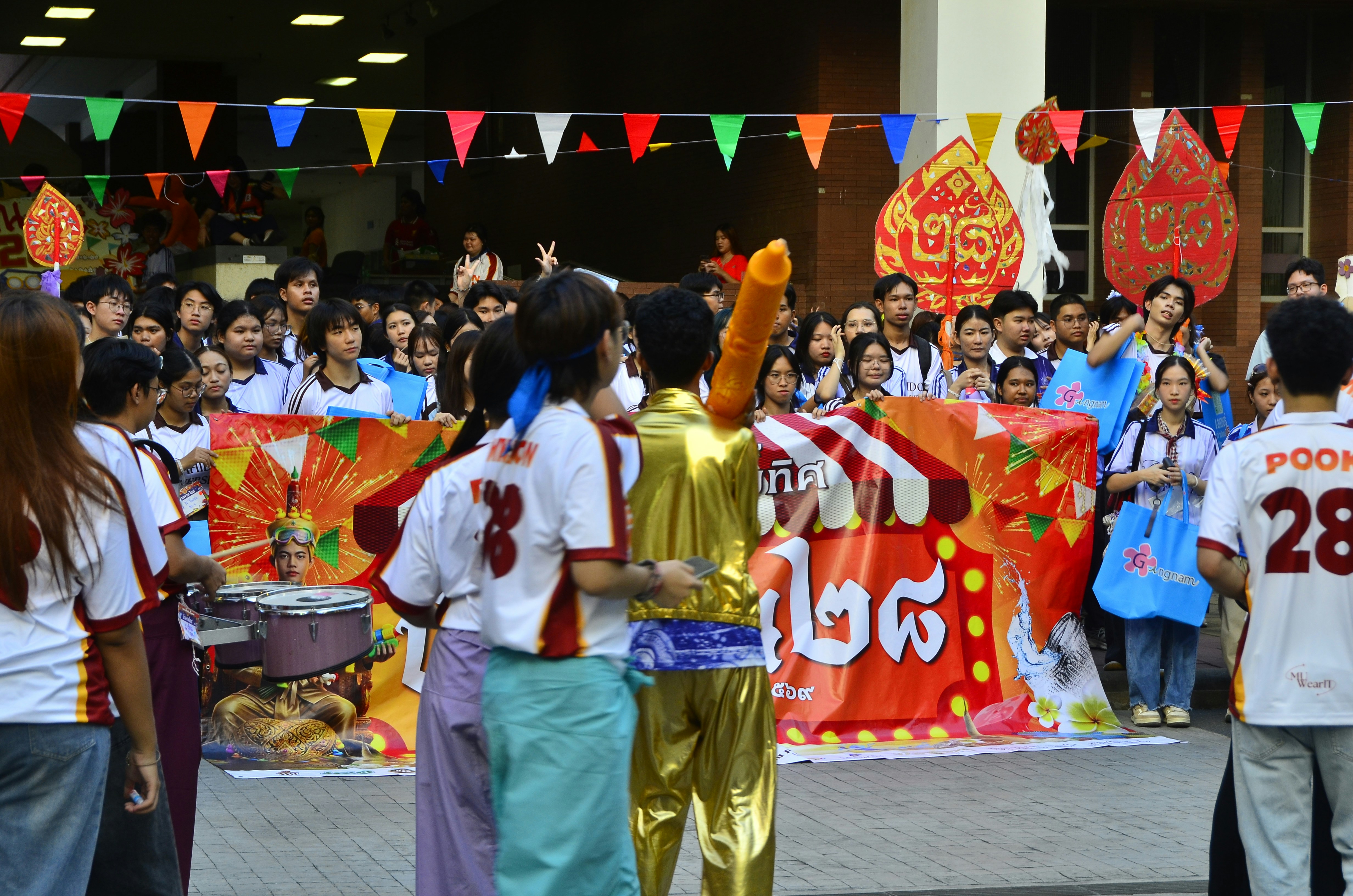 Festival Crowd Fanfare: Gold-clad Performer Faces Off Against Colorful Parade Banner