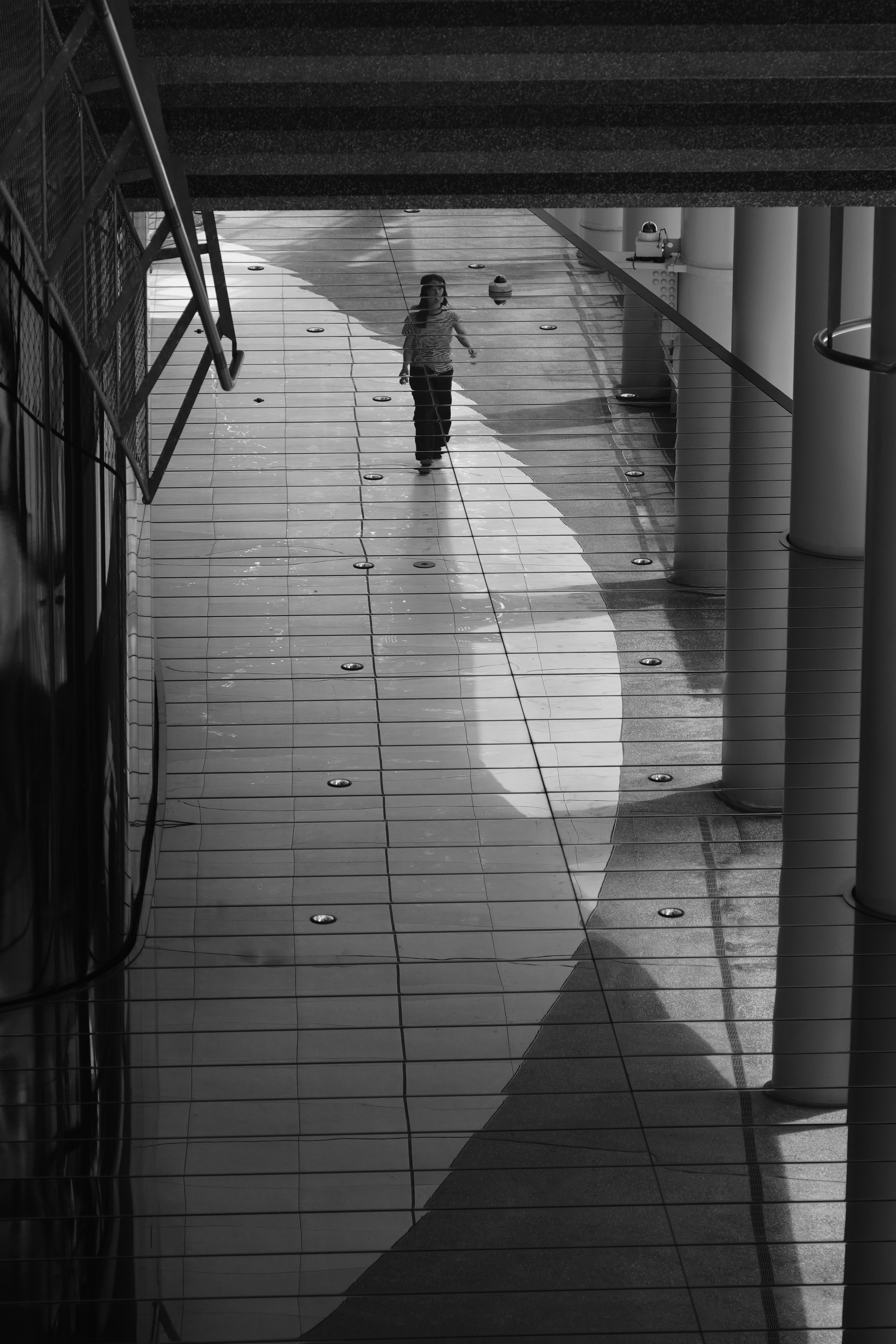 Shadowed Path: A solitary figure in a curved, tiled corridor
