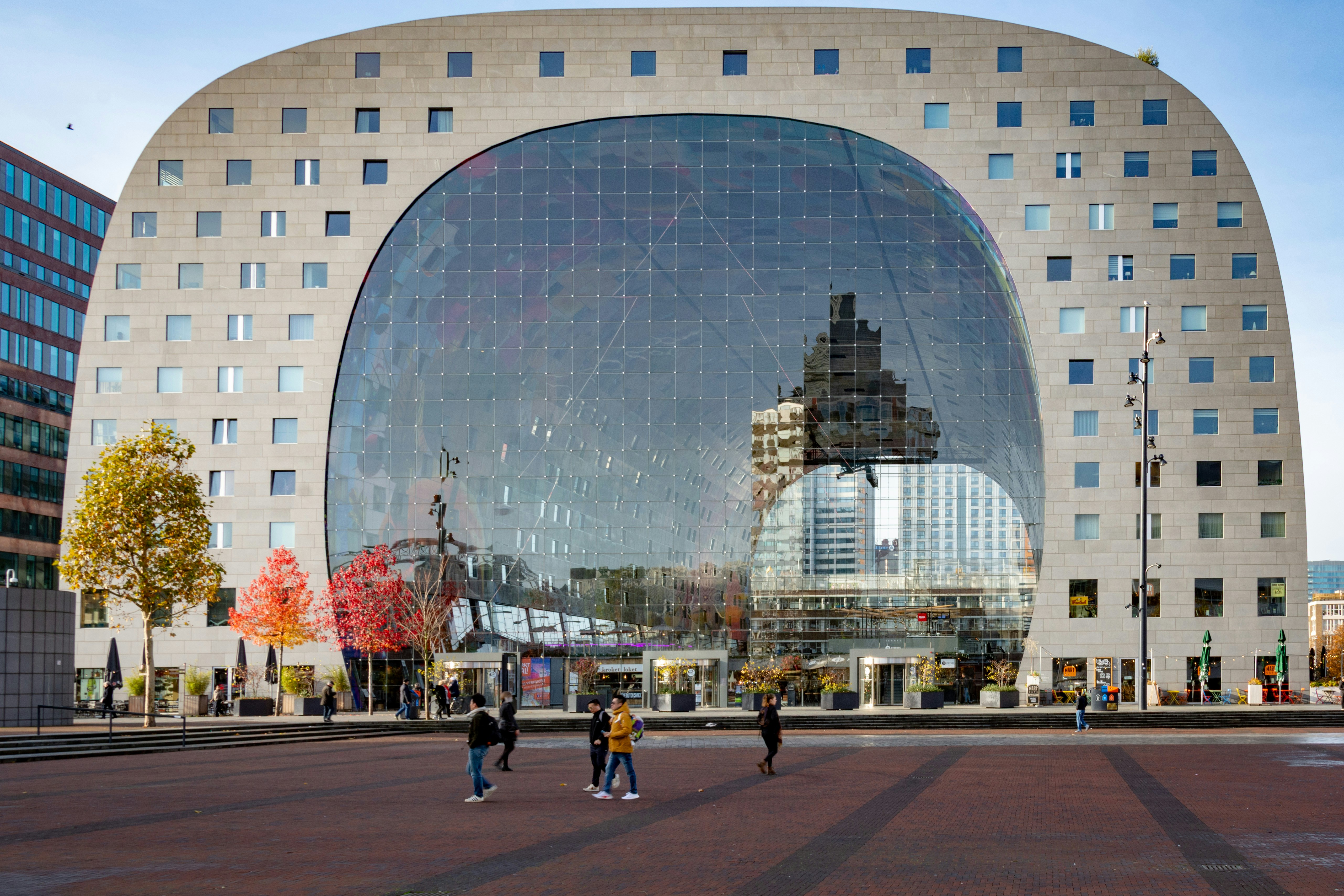 Modern building with a large rounded glass center reflecting surrounding skyscrapers; pedestrians and trees in foreground add scale and life.