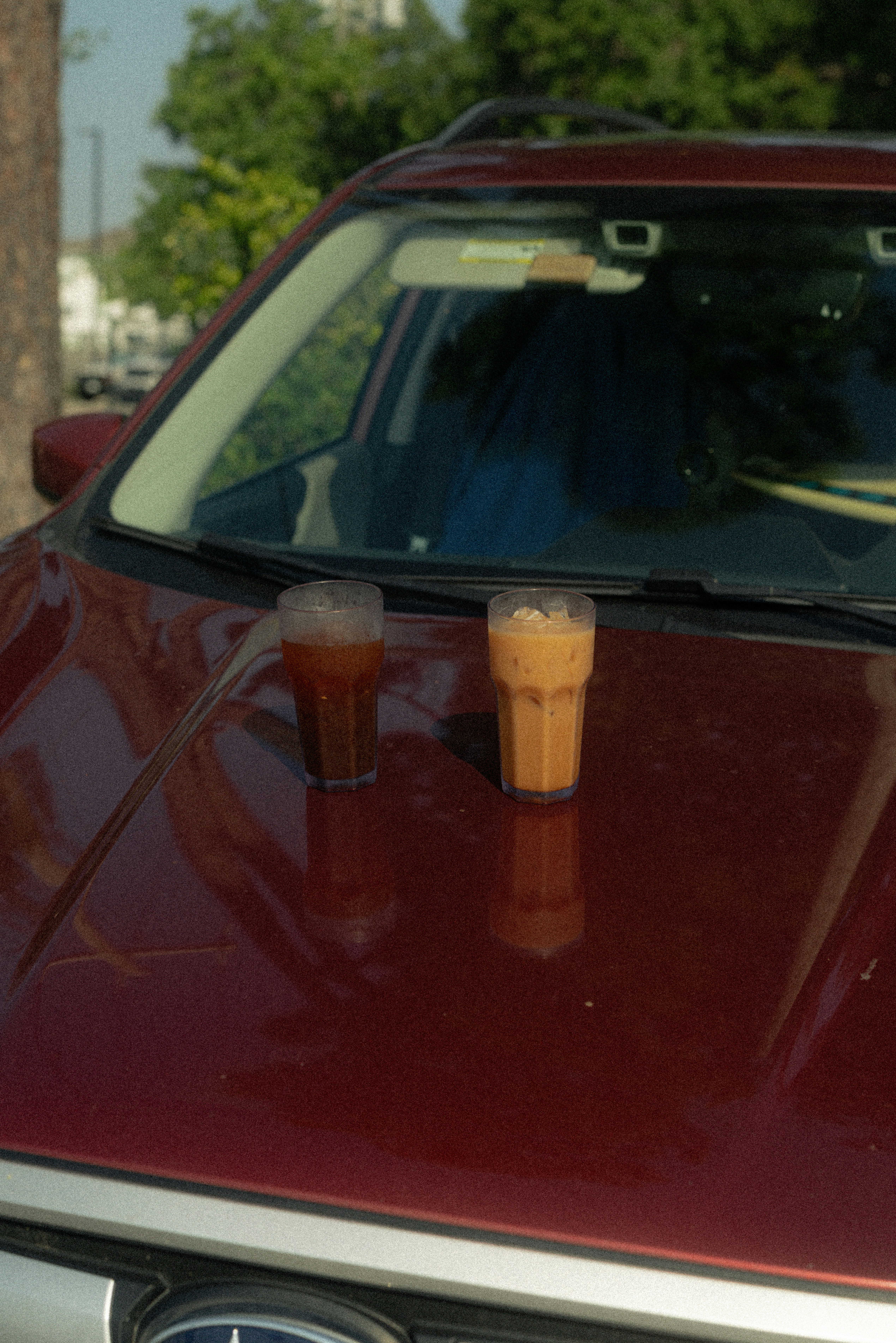 Two frothy beverages on a maroon car hood under sunlight