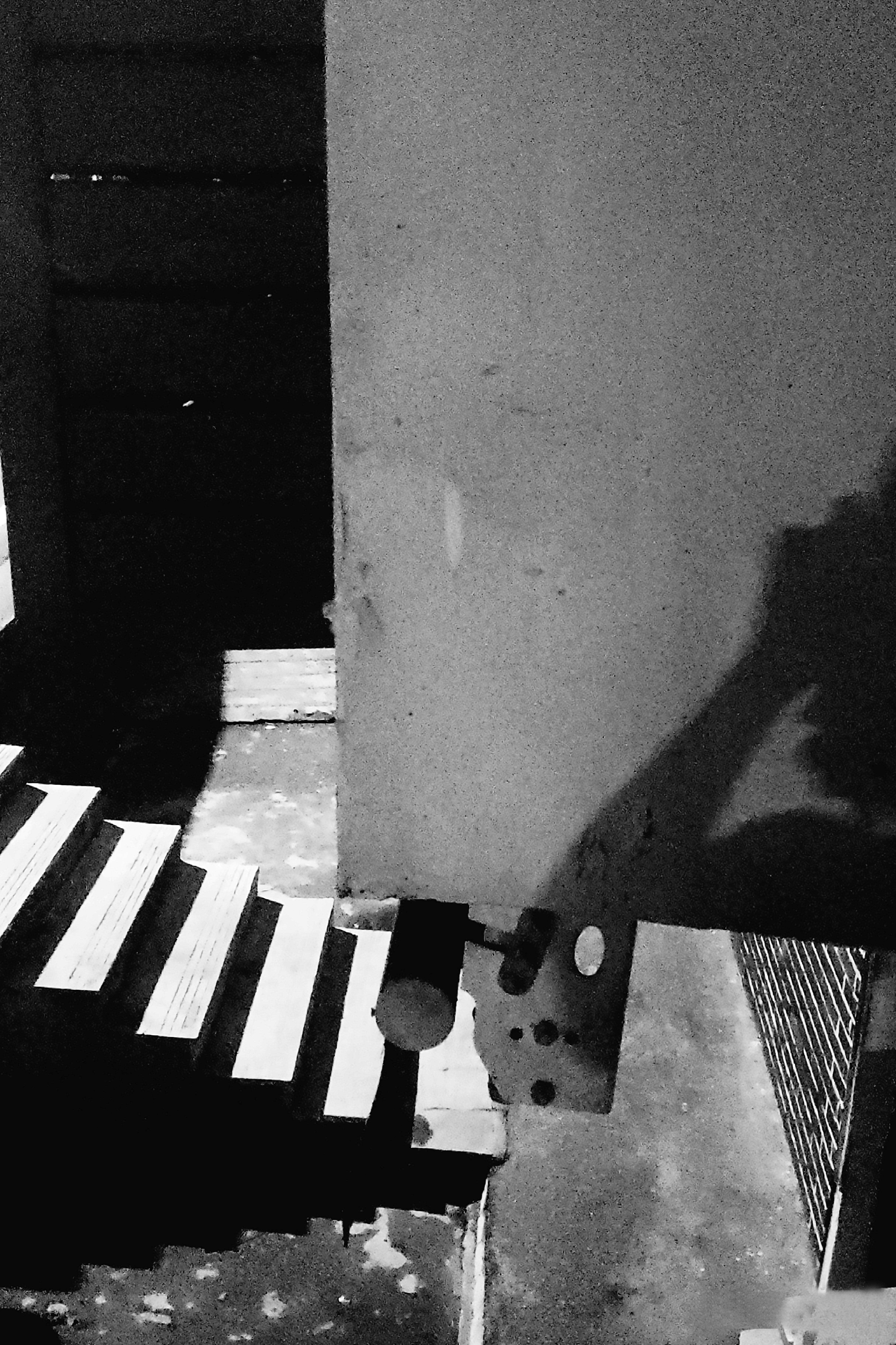 Staircase descending into a dark doorway, captured in high-contrast grayscale with strong shadows and concrete textures.