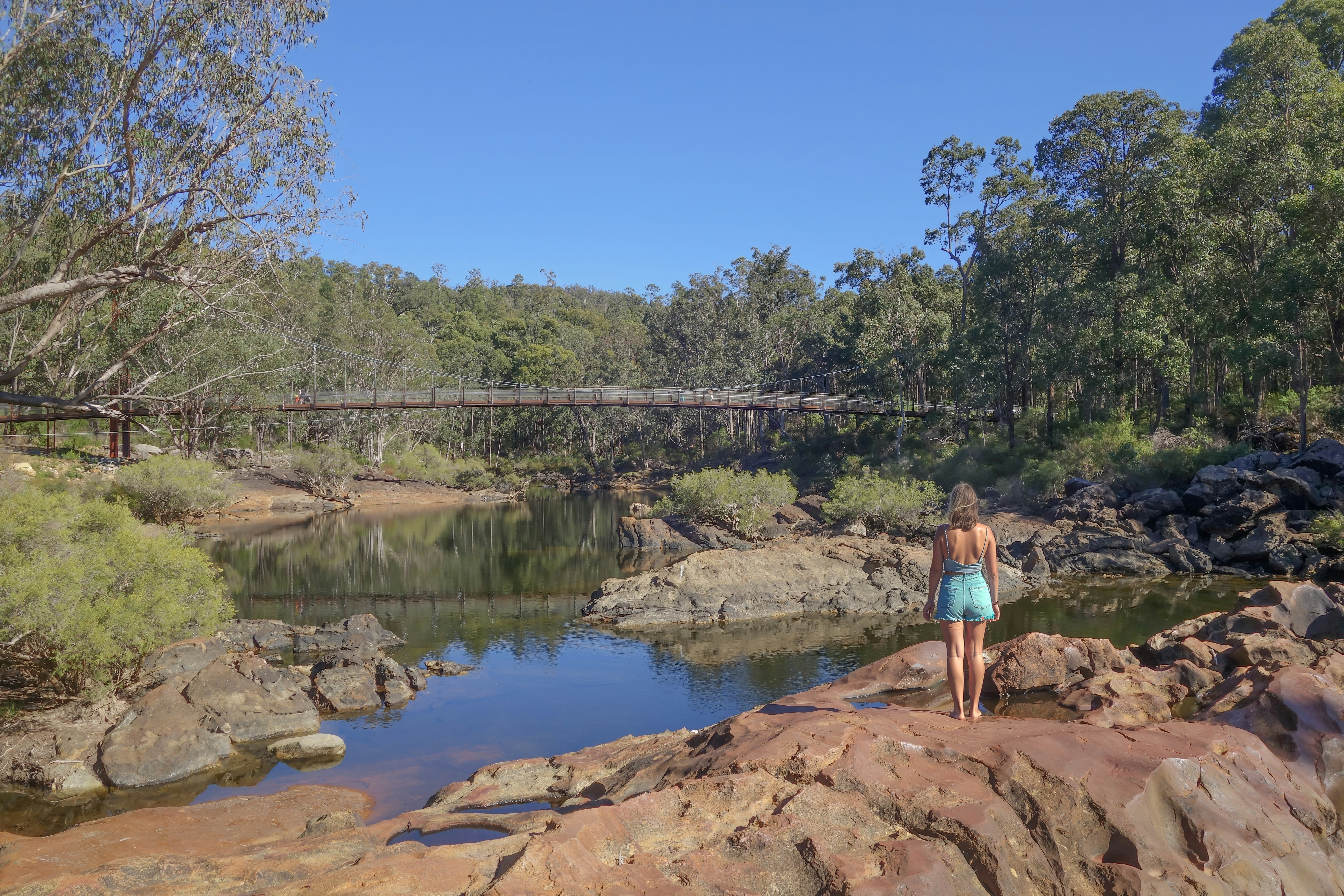 Woman in turquoise shorts gazes toward a rocky riverbank under a clear blue sky