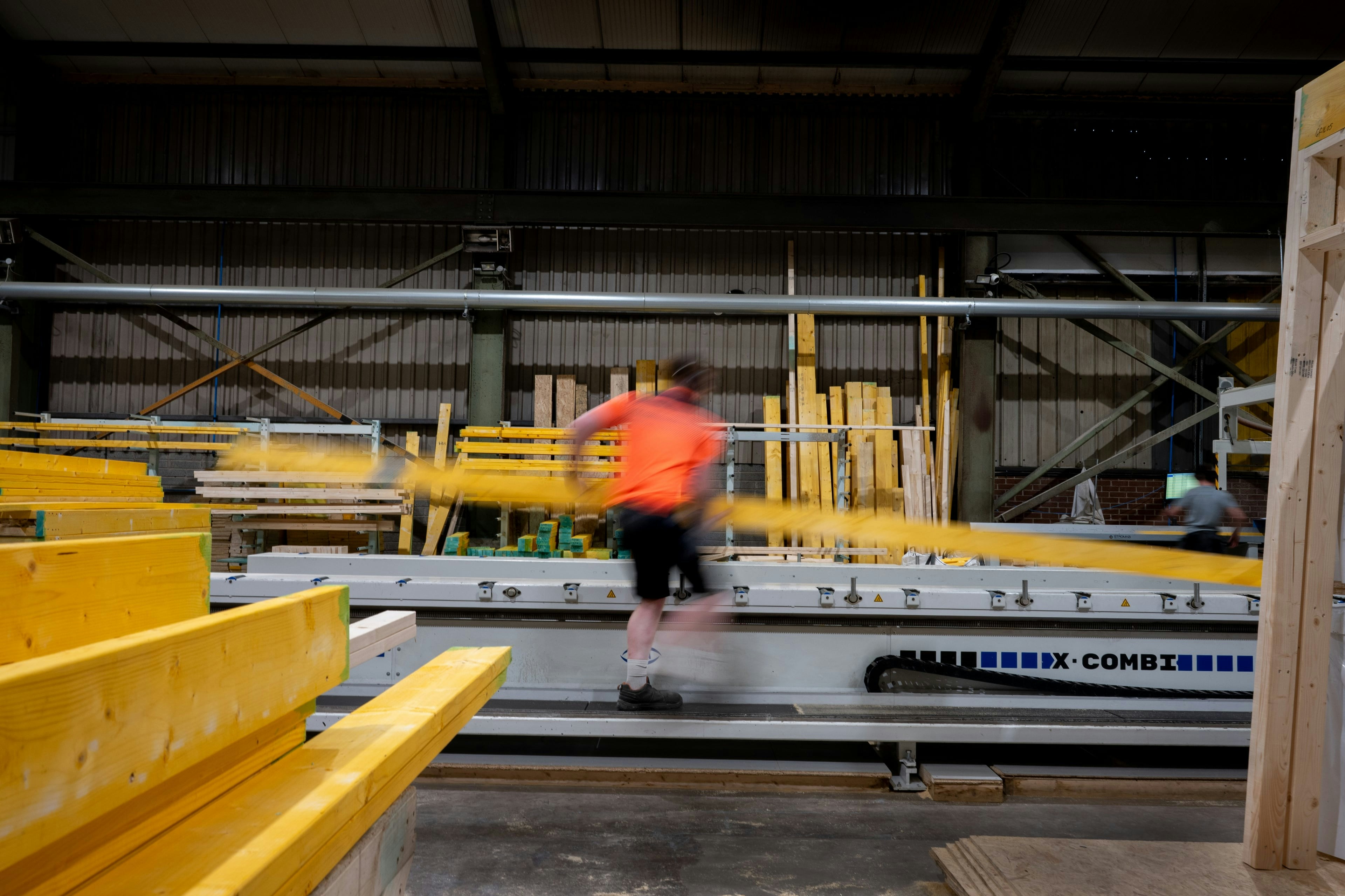 Athletic figure in bright orange shirt moves quickly along a box-laden industrial track inside a warehouse; motion blur emphasizes speed and activity.