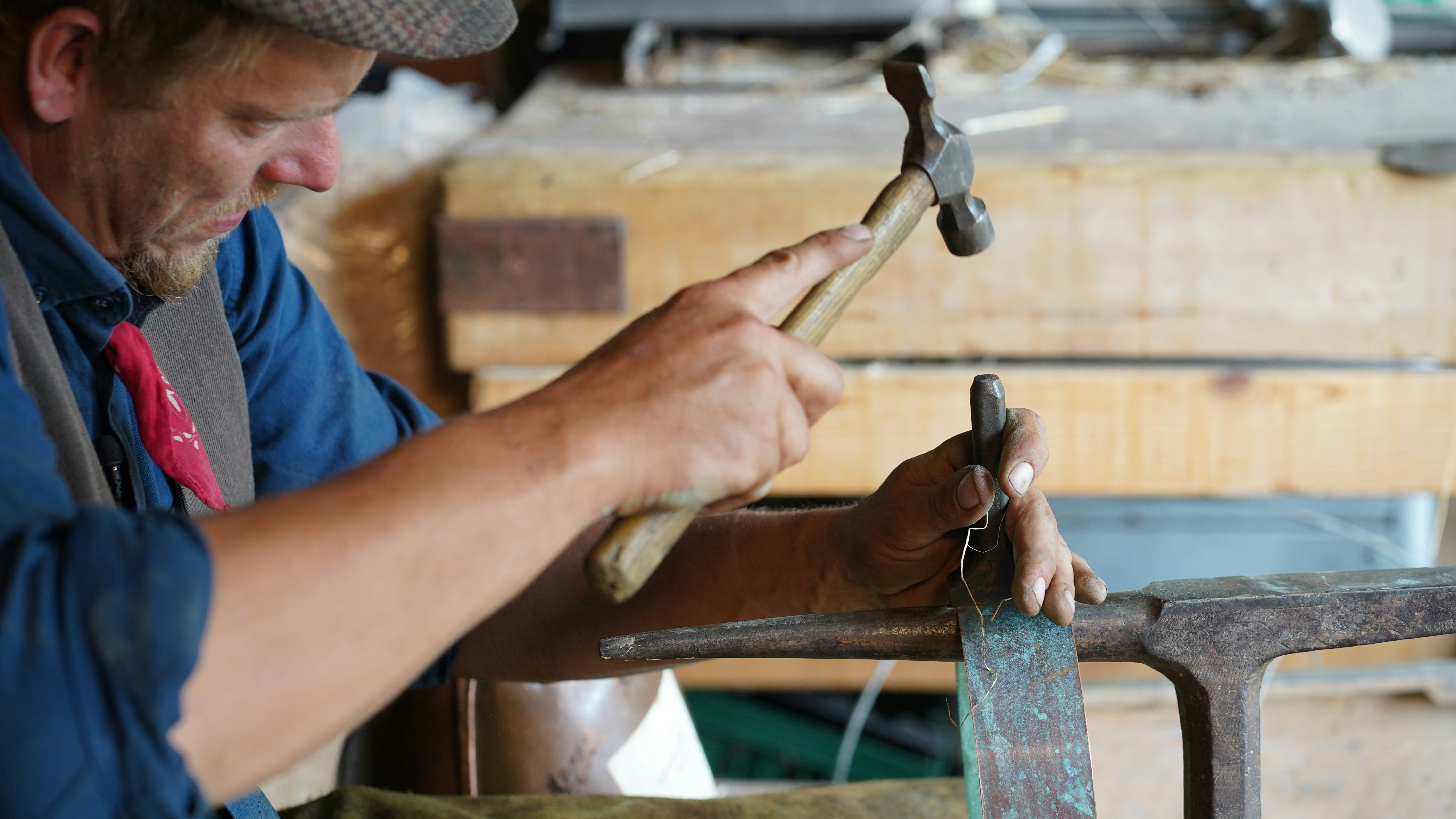 A person hammering a metal strip on an anvil in a workshop