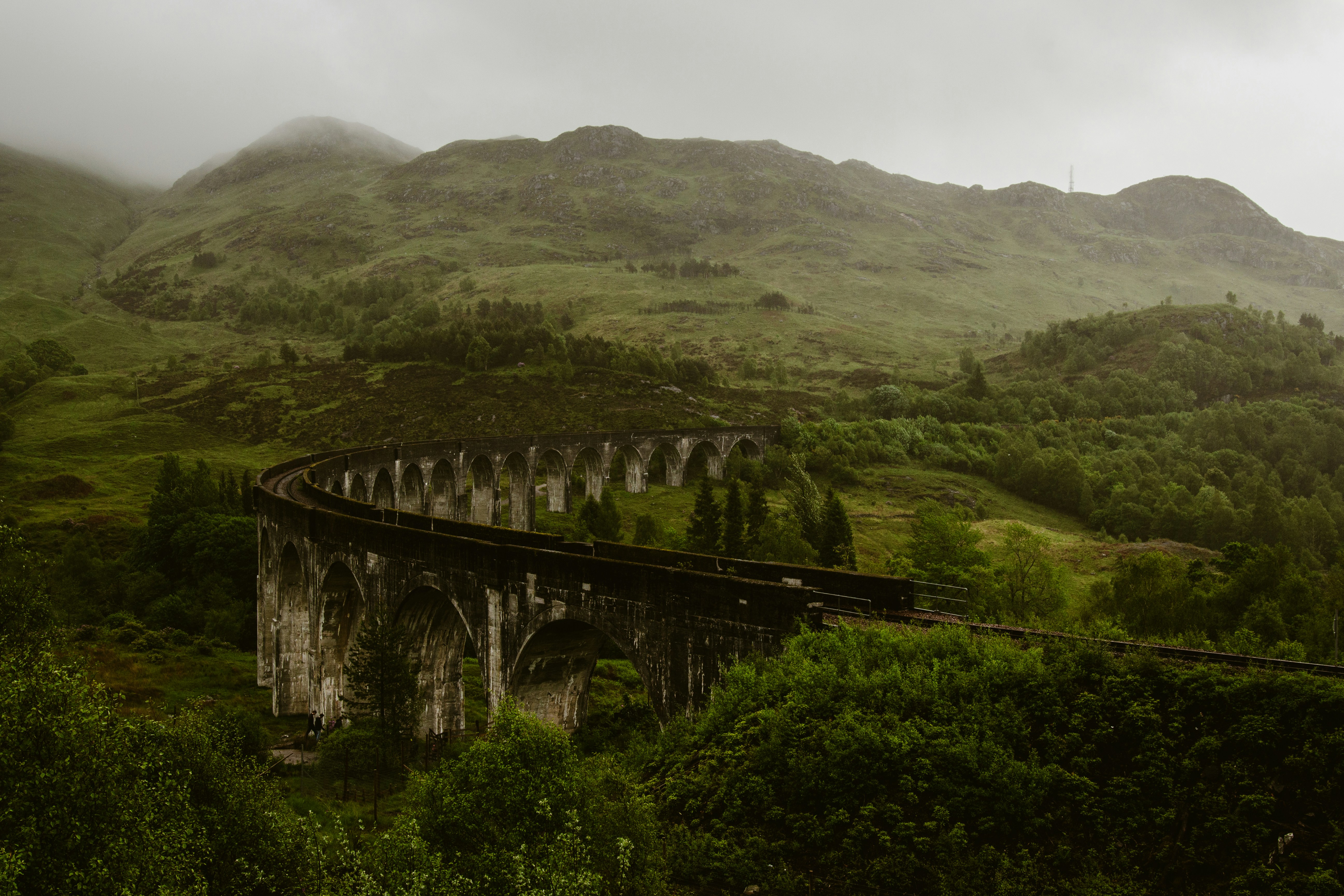 The Glenfinnan Viaduct curving through a misty green landscape in the Scottish Highlands