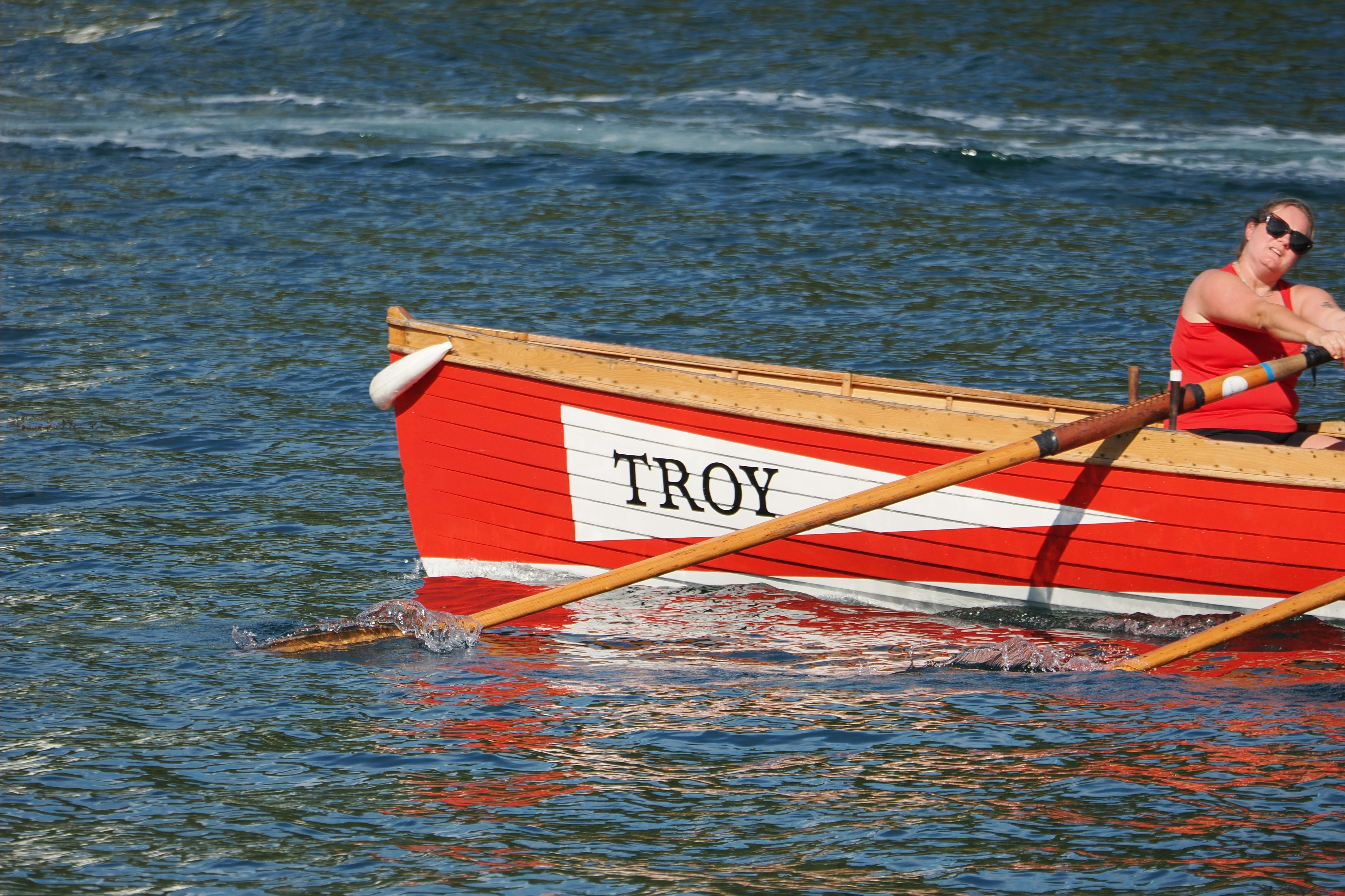 A woman in a red tank top rowing a red boat named TROY