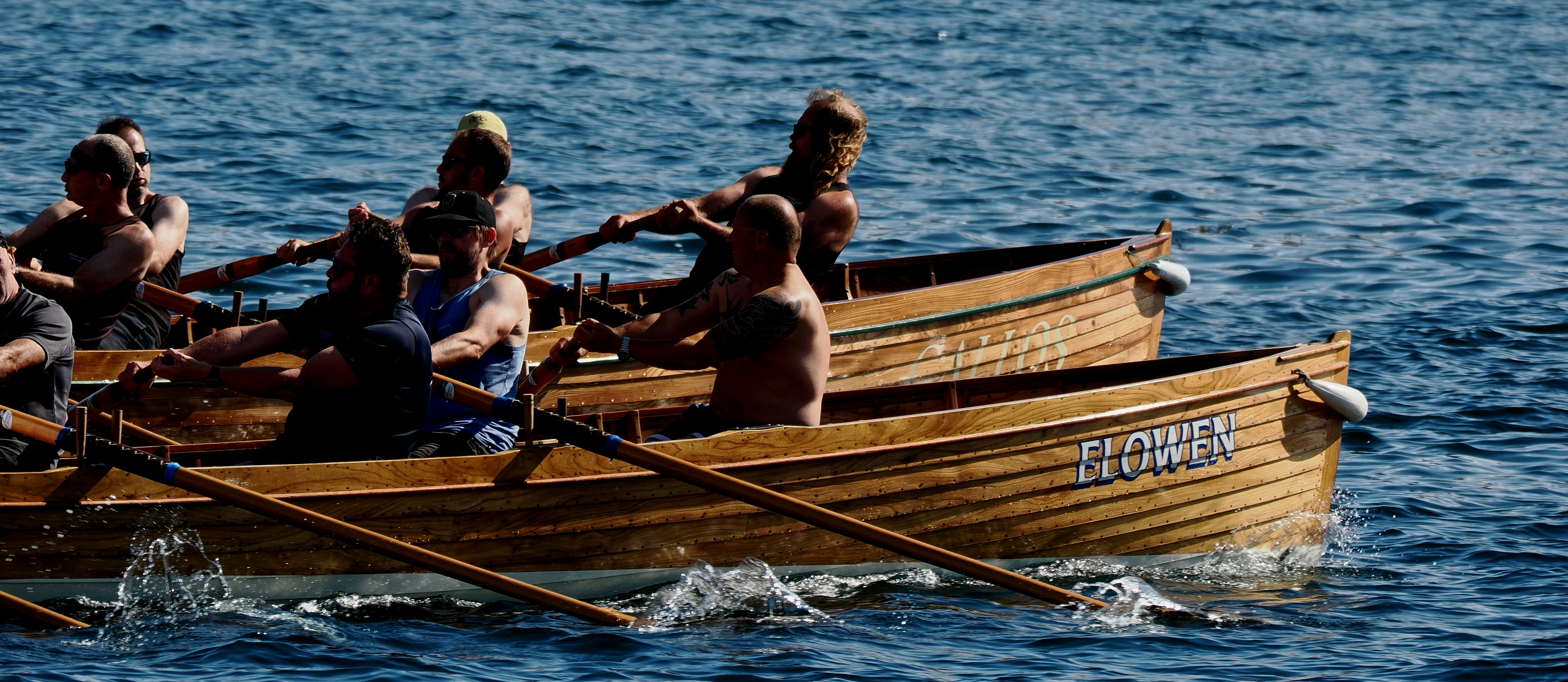 Rowers in synchronized wake cutting through blue