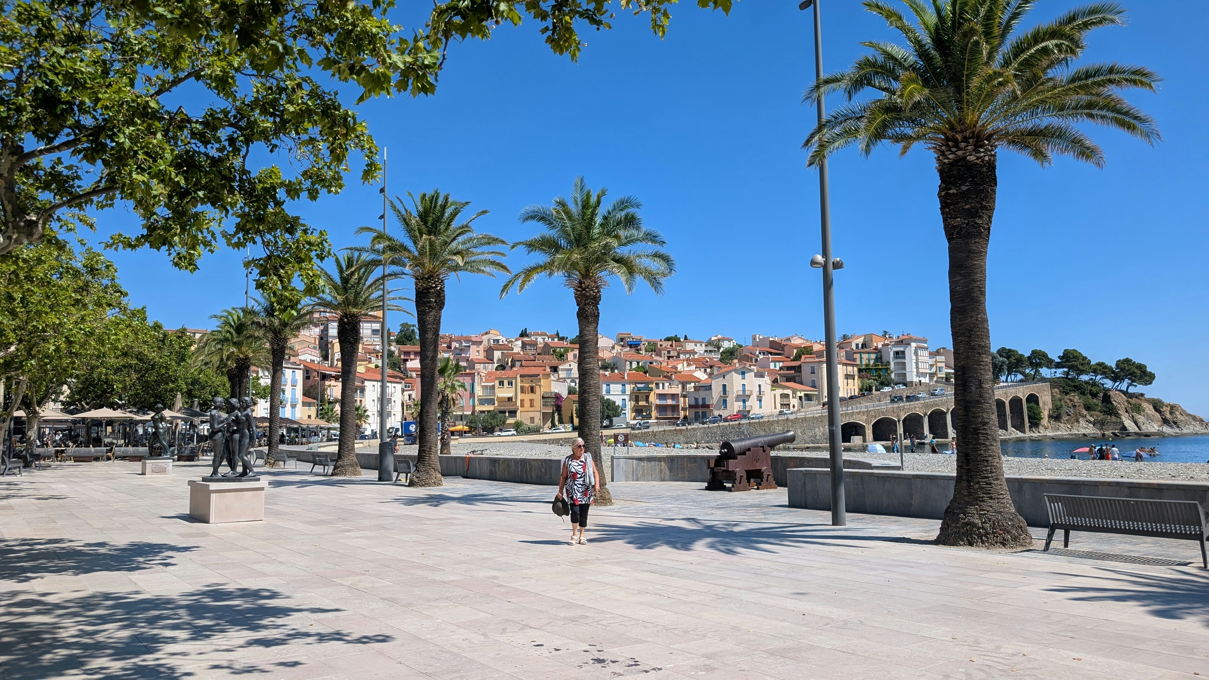 Harborfront promenade with distant village under a clear blue sky