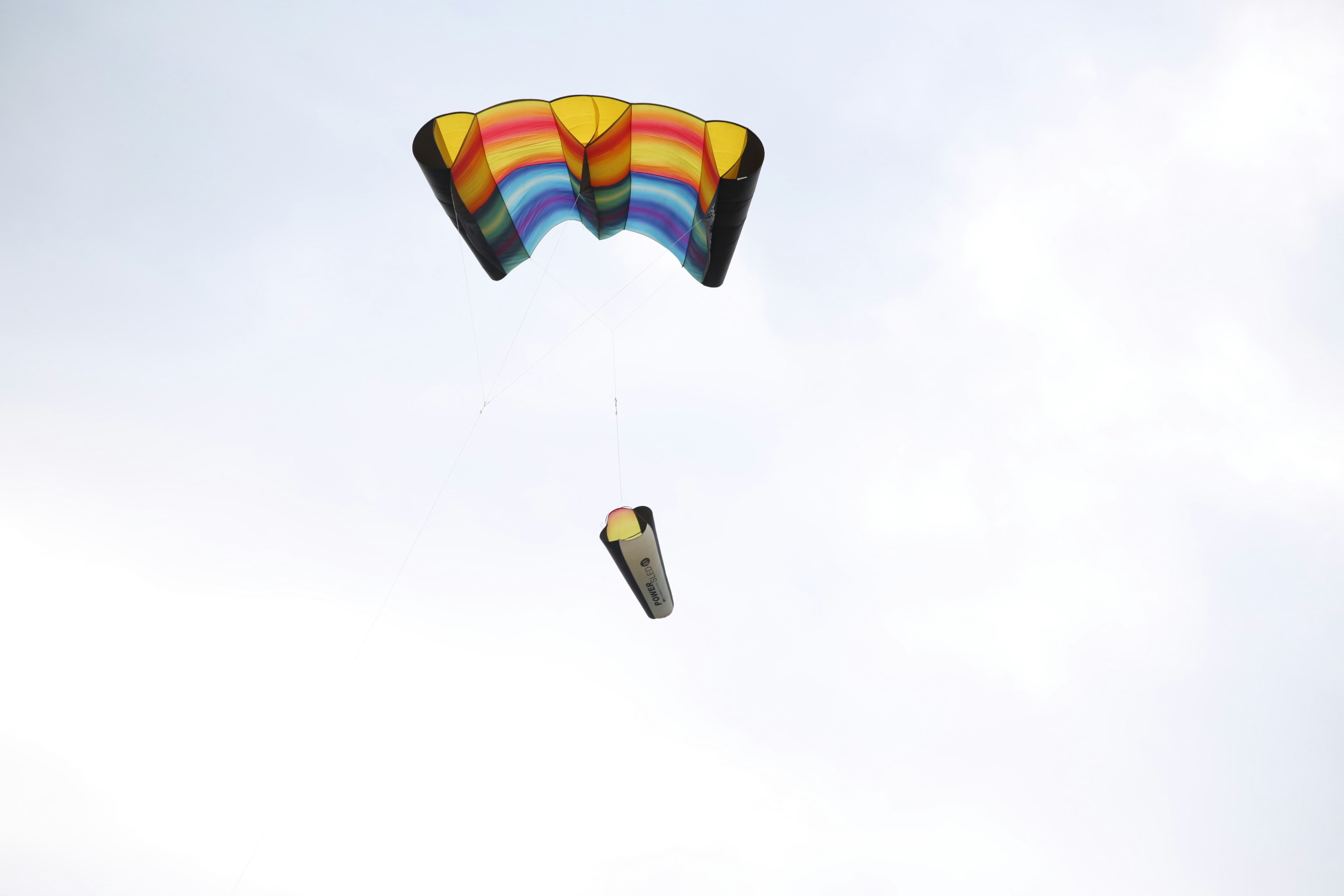 Rainbow parachute gliding above a lone descending rider
