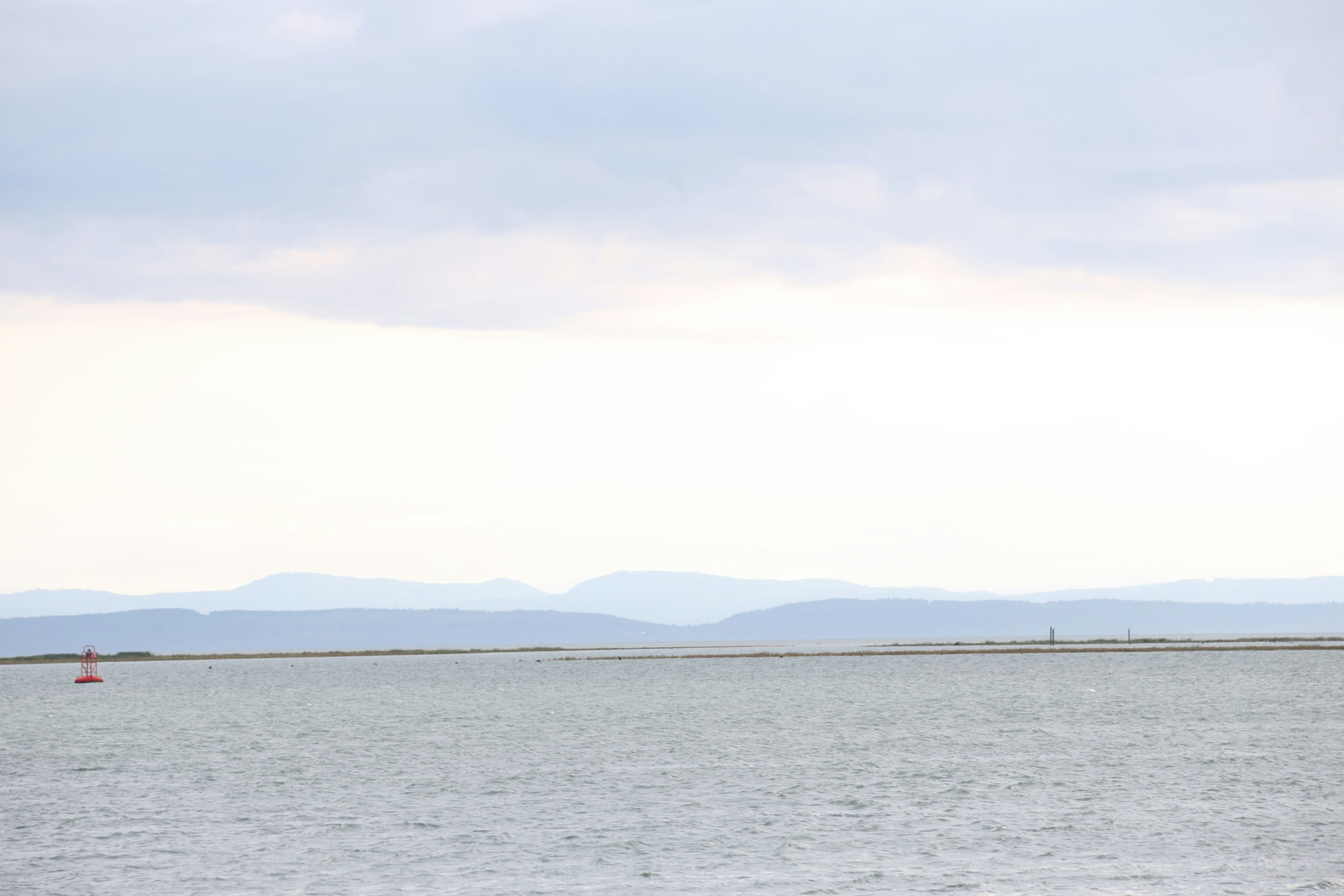 Quiet Sea Horizon with Distant Islands and a Red Buoy