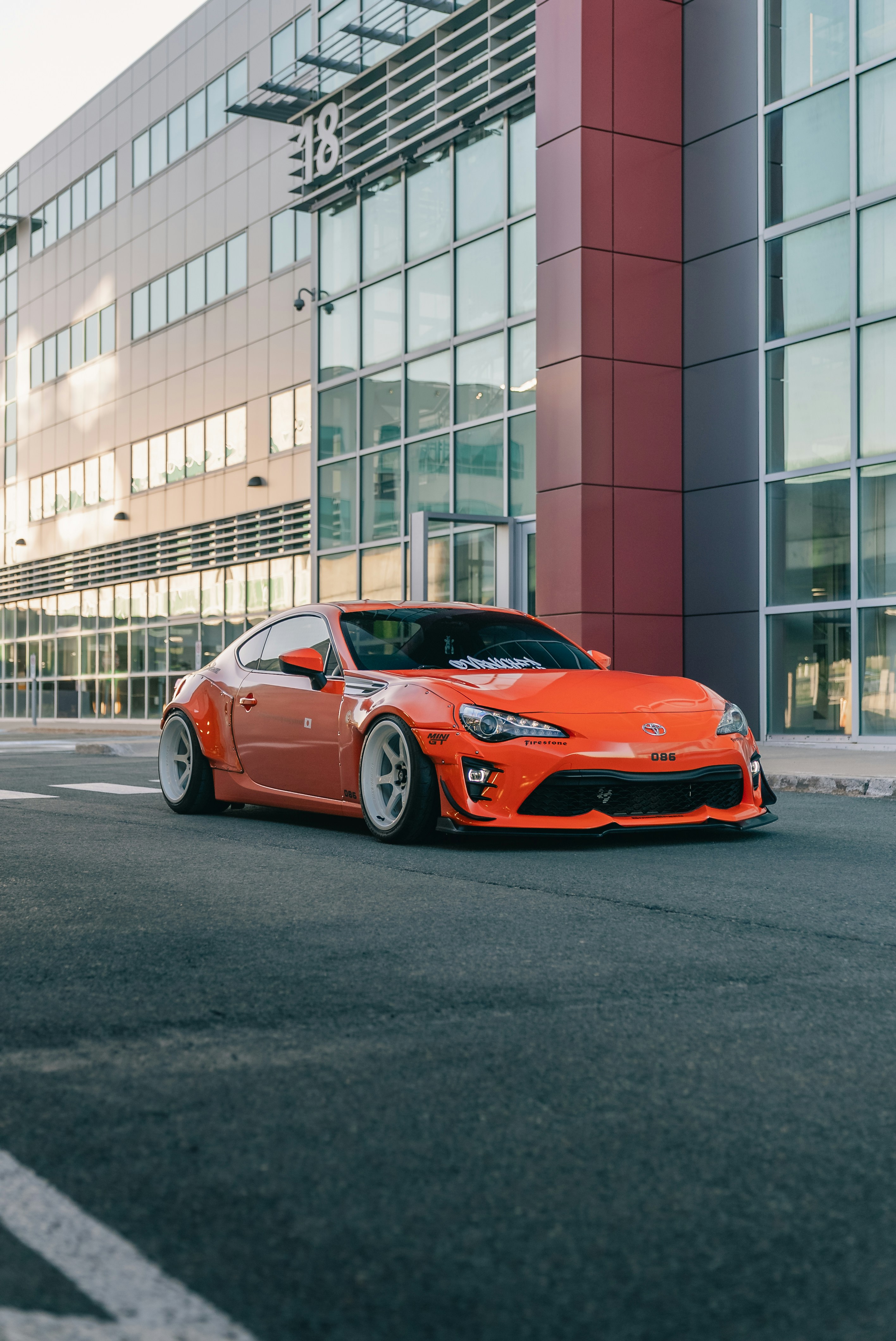 Orange Drift: A Low-A Angle Glimpse of a Sport Coupe Beside a Modern Glass Facade