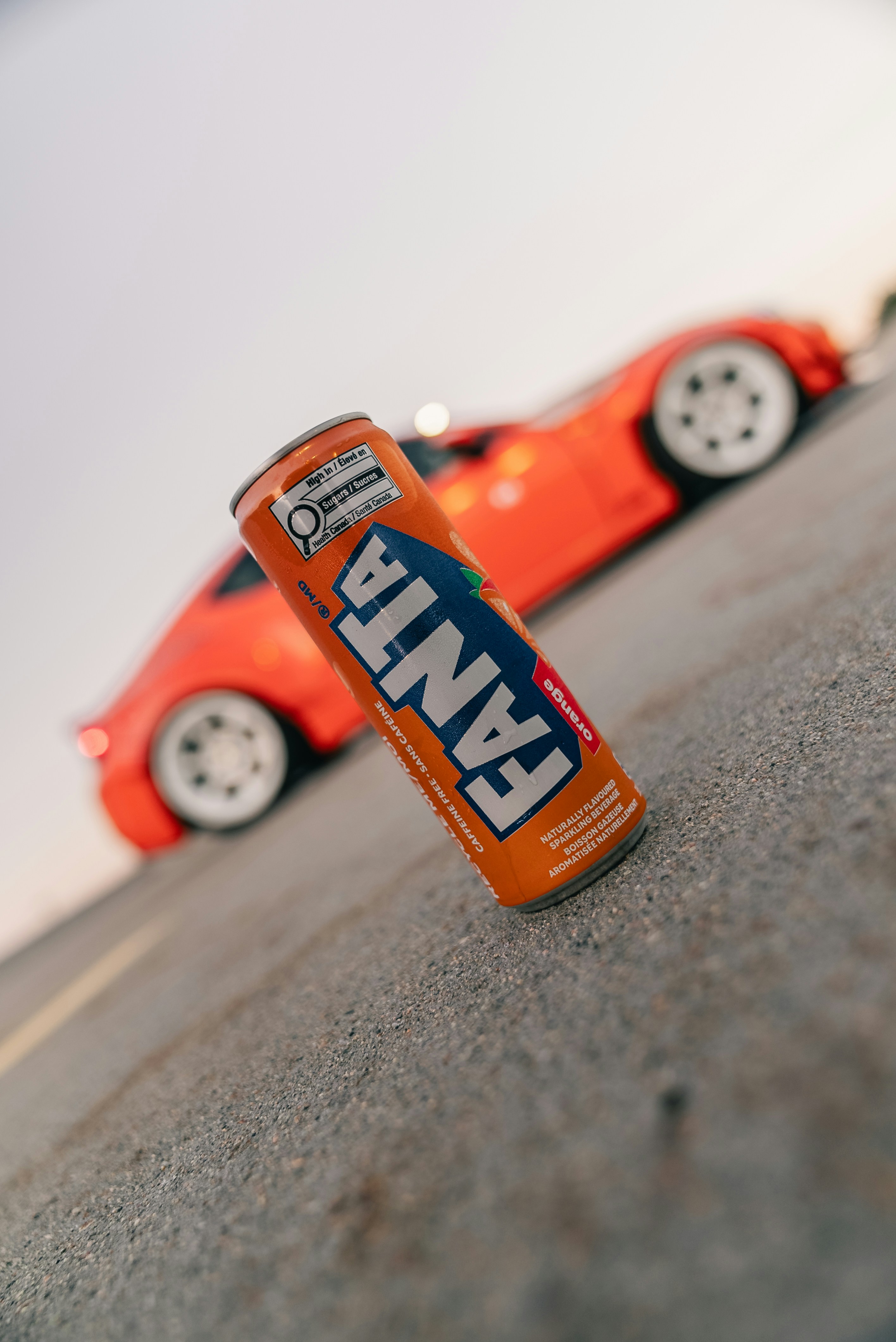 Orange Can, Red Car, and a Tilted Scene on Asphalt
