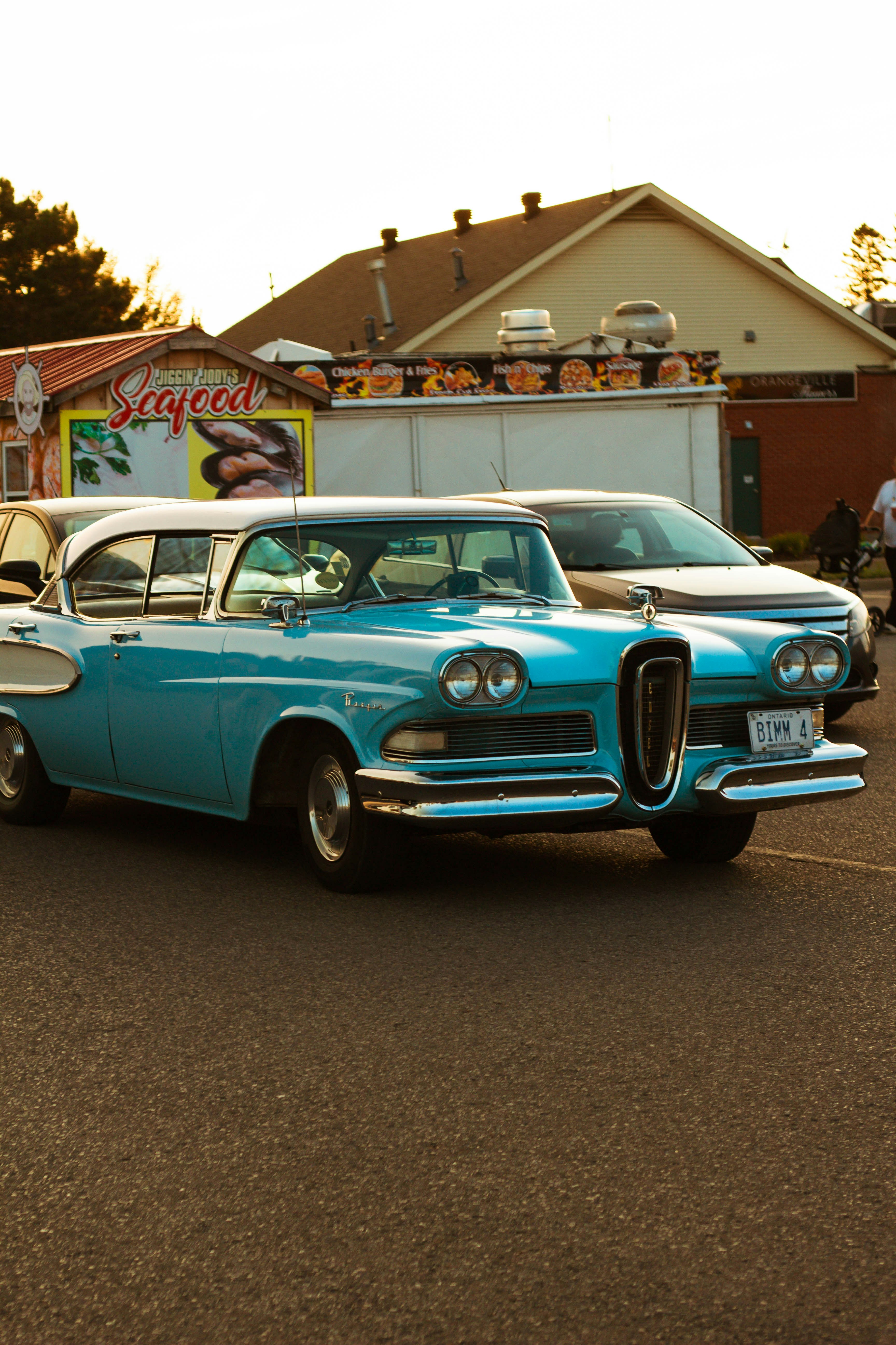 Blue vintage car with chrome accents anchors a casual street scene featuring a diner-style seafood sign and another modern car in the background.