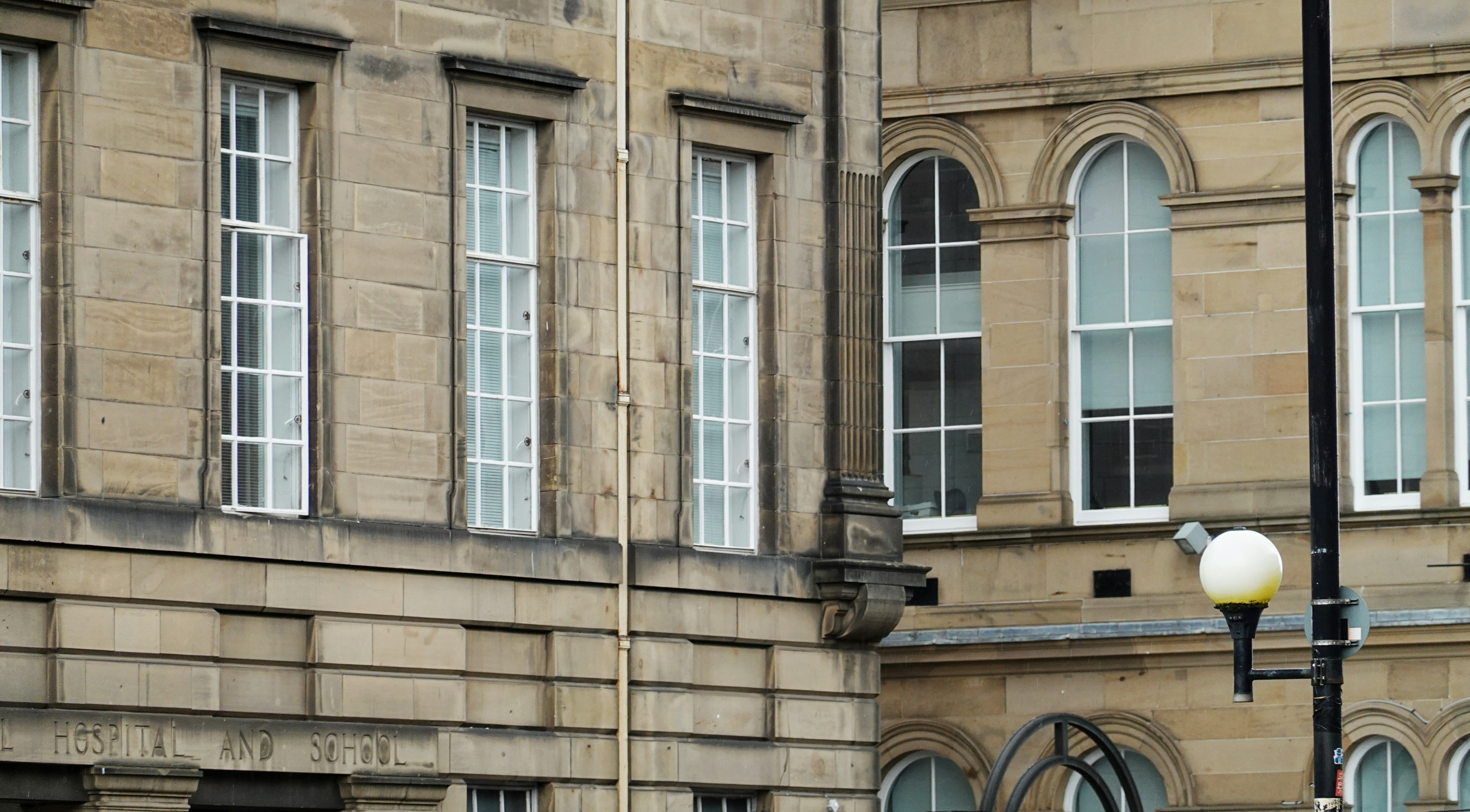 Stone building facade with tall sash windows and arched detailing, a streetlamp in the foreground adds urban texture.