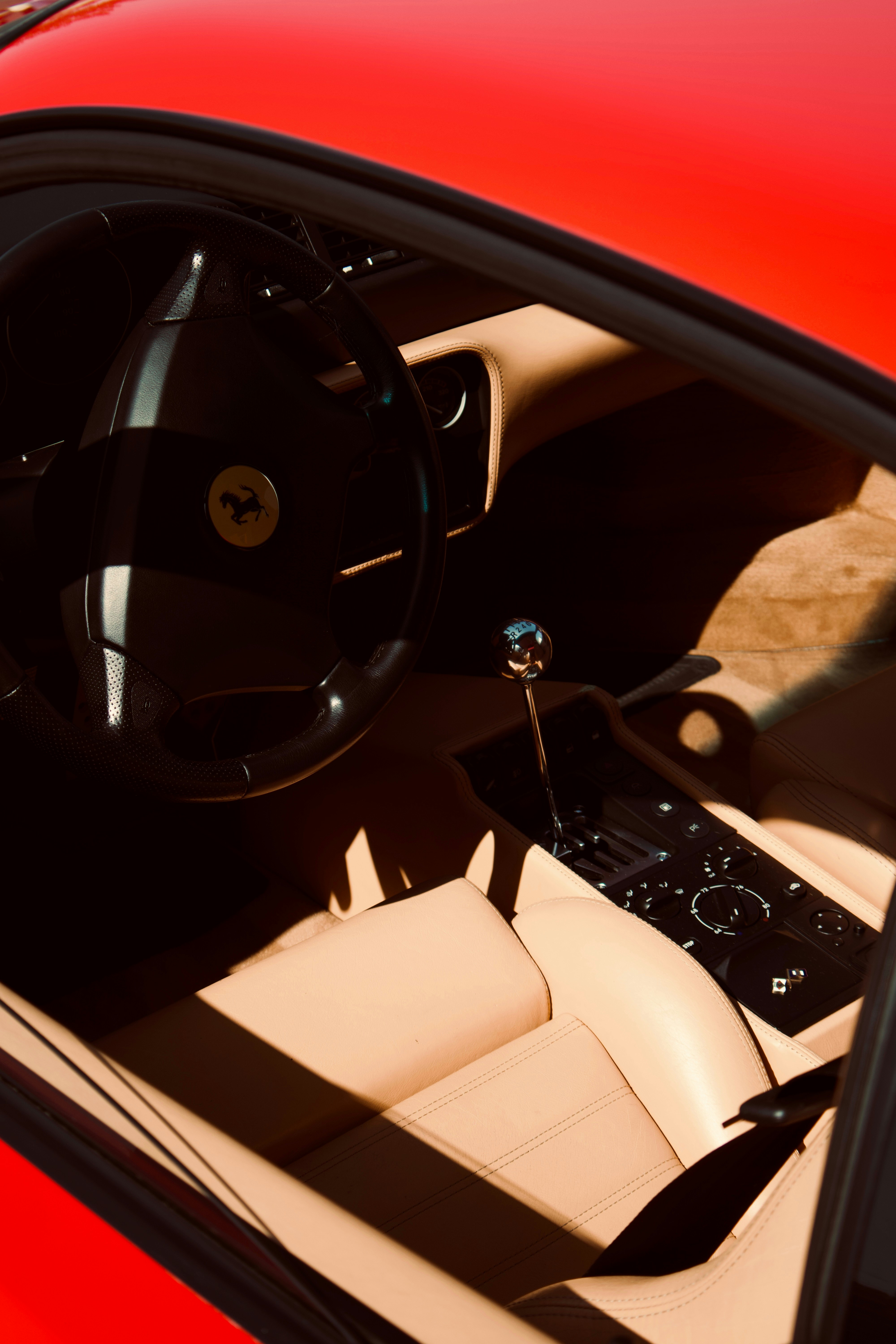 Sleek red car interior with tan leather seats and a prominent Ferrari steering wheel bathed in warm light.