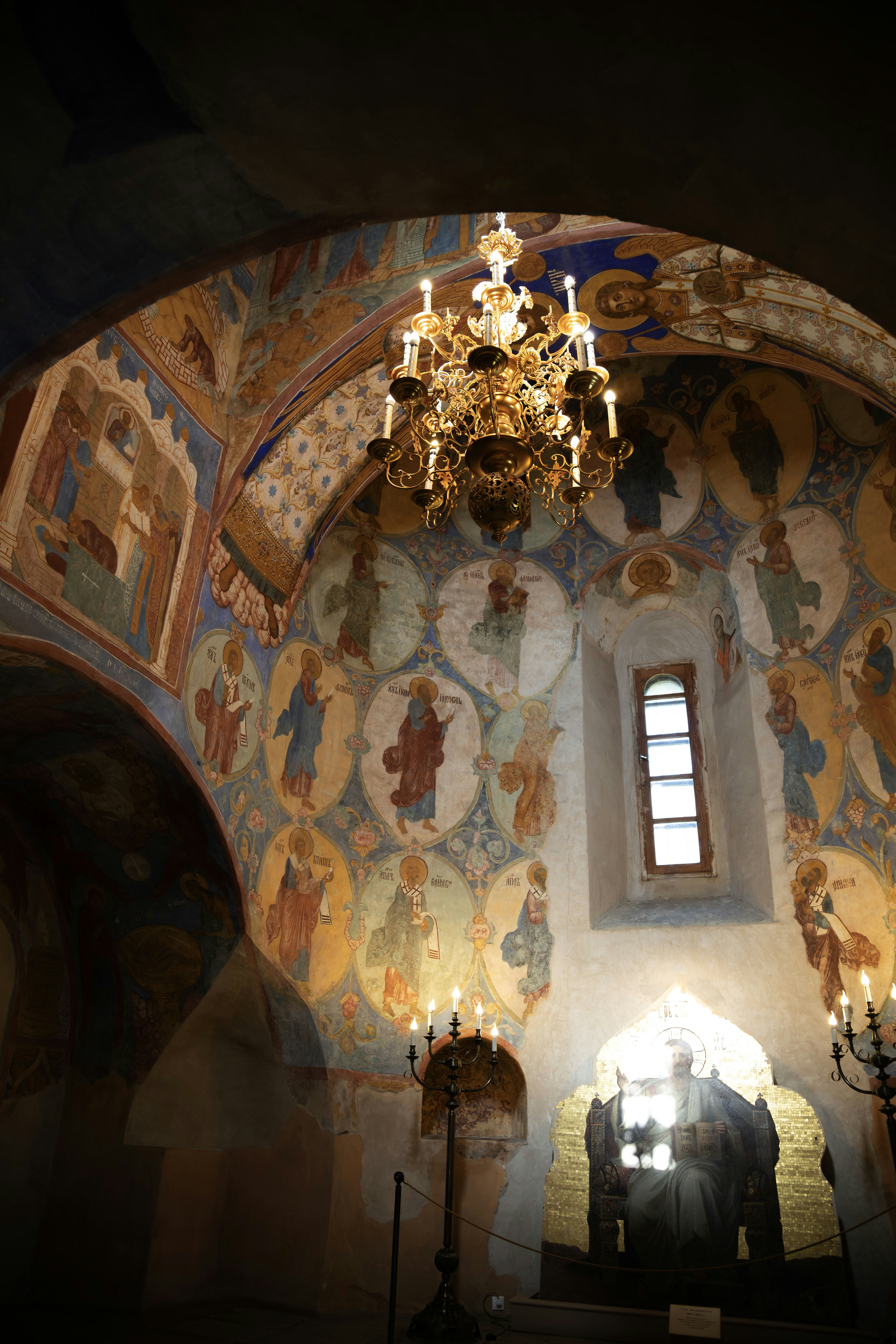 Charmed Chapel: A Medieval Fresco Parade Beneath a Glittering Candelabrum