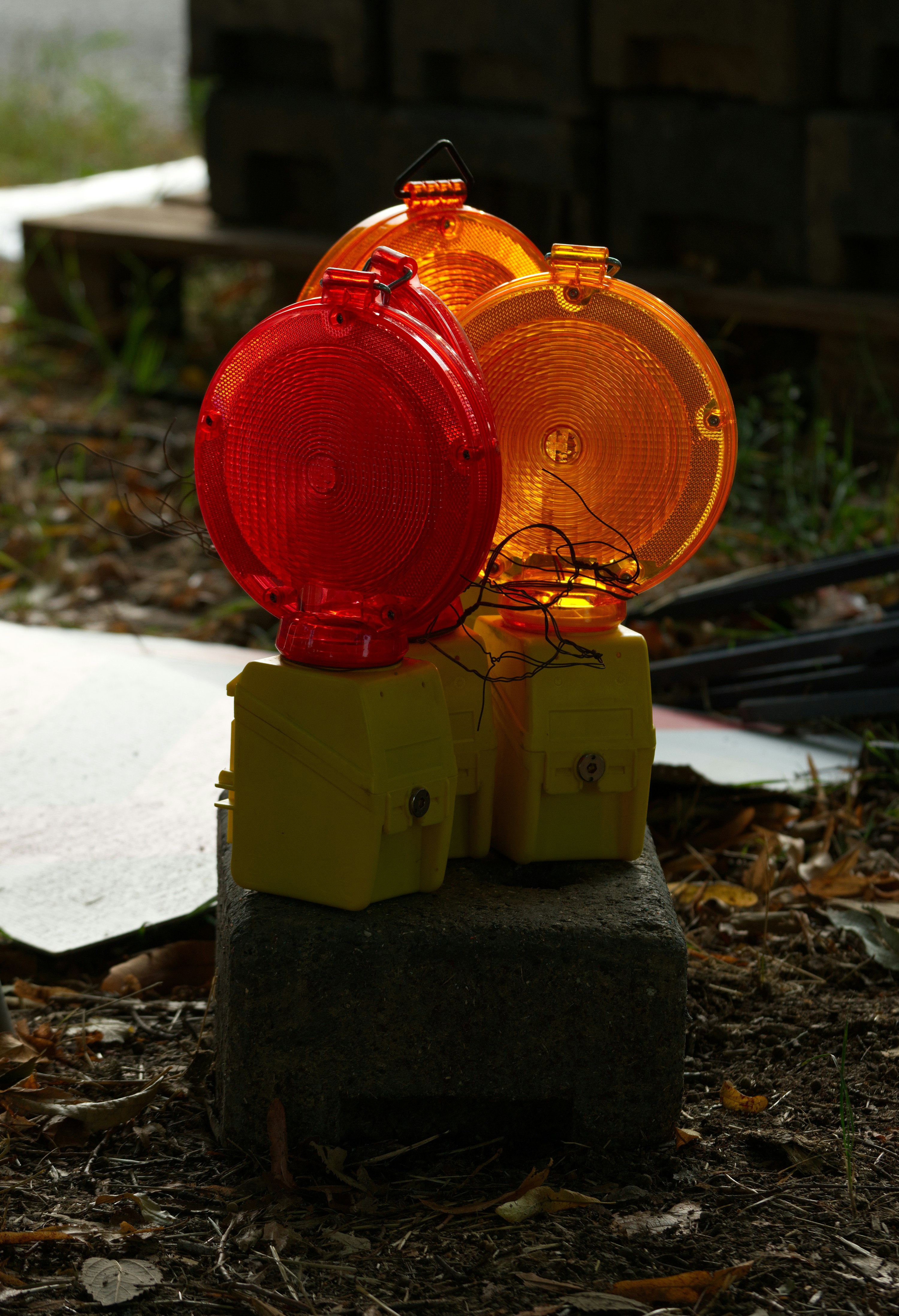 Two stacked warning lights with red and amber lenses sit atop yellow bases on a concrete block in an outdoor, slightly cluttered work area.