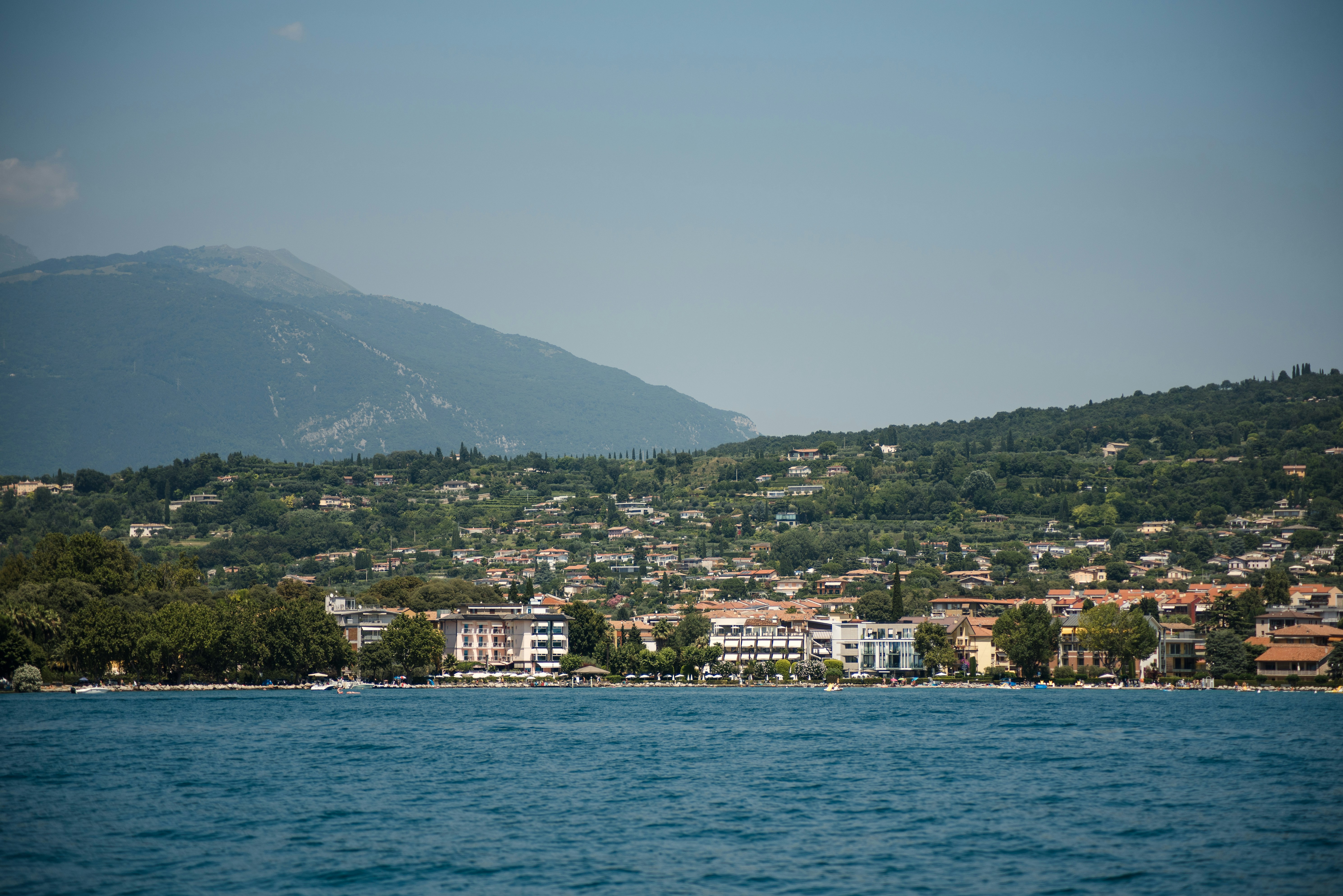Coastal town between blue sea and green hills under a distant mountain