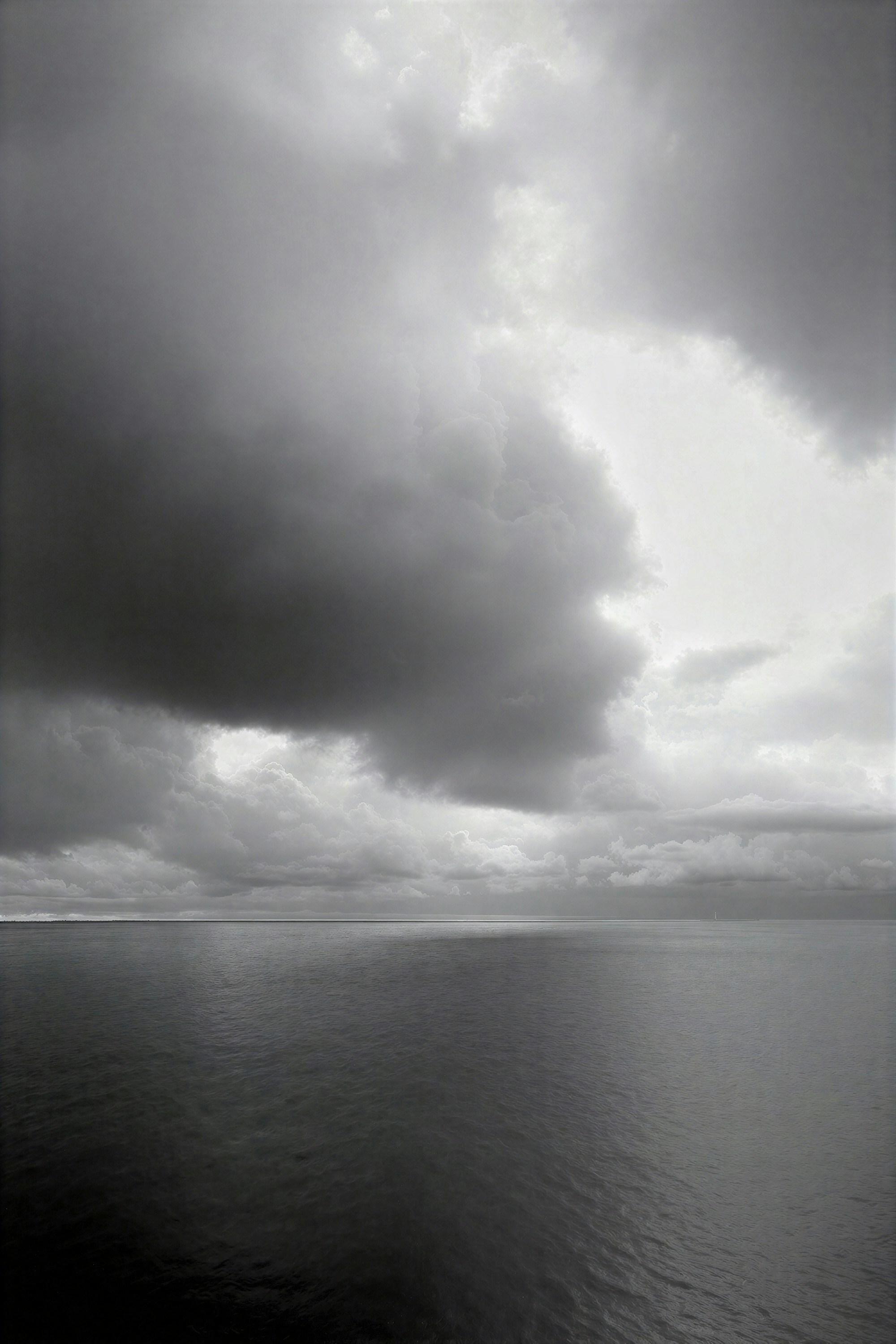 Monochrome seascape with a dramatic, looming cloudbank over a calm, expansive ocean; minimalism and tonal range emphasize mood and space.