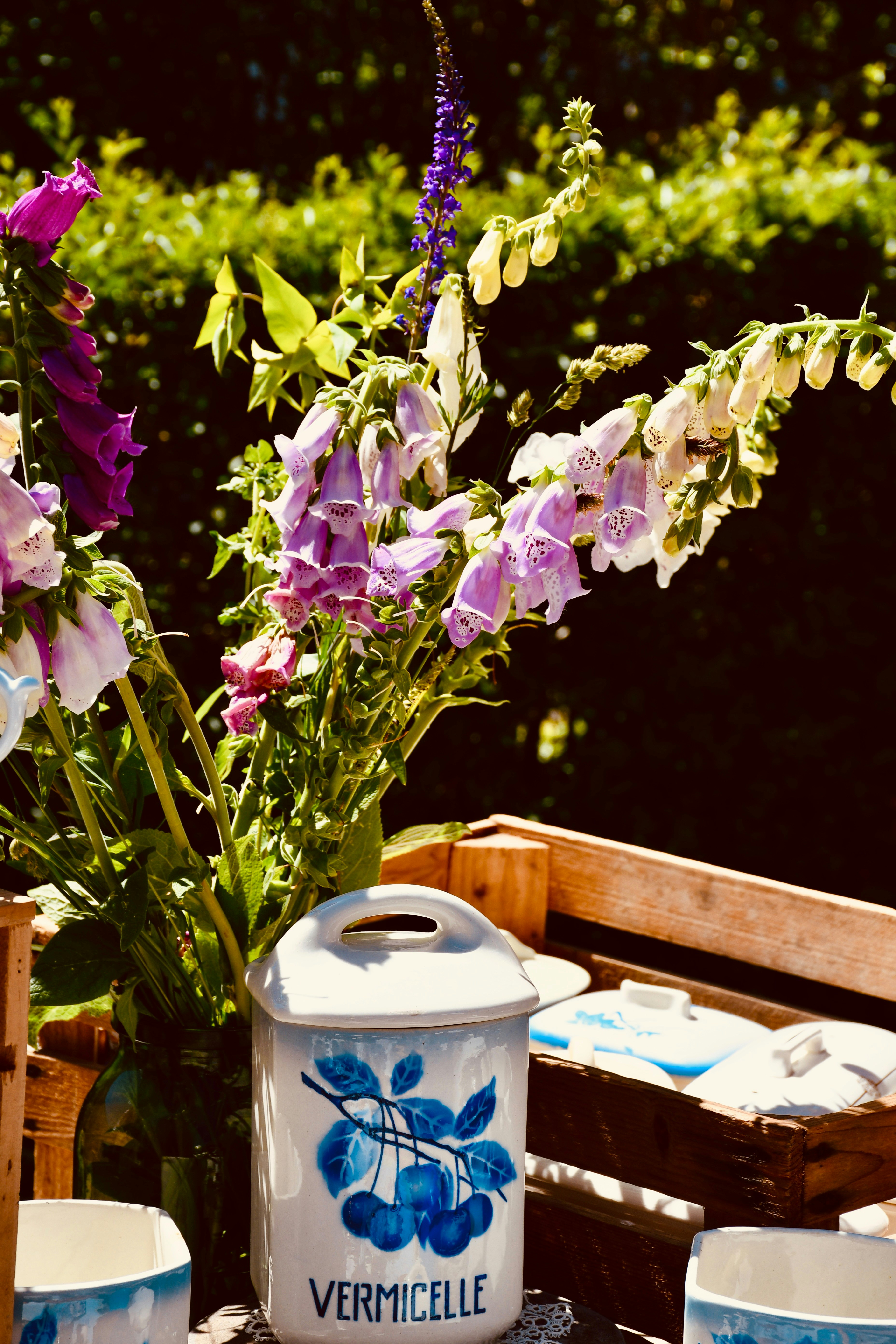 A Rustic Still-Life Parade: Flowers, Blue Ceramic Jar, and Weathered Wooden Deck