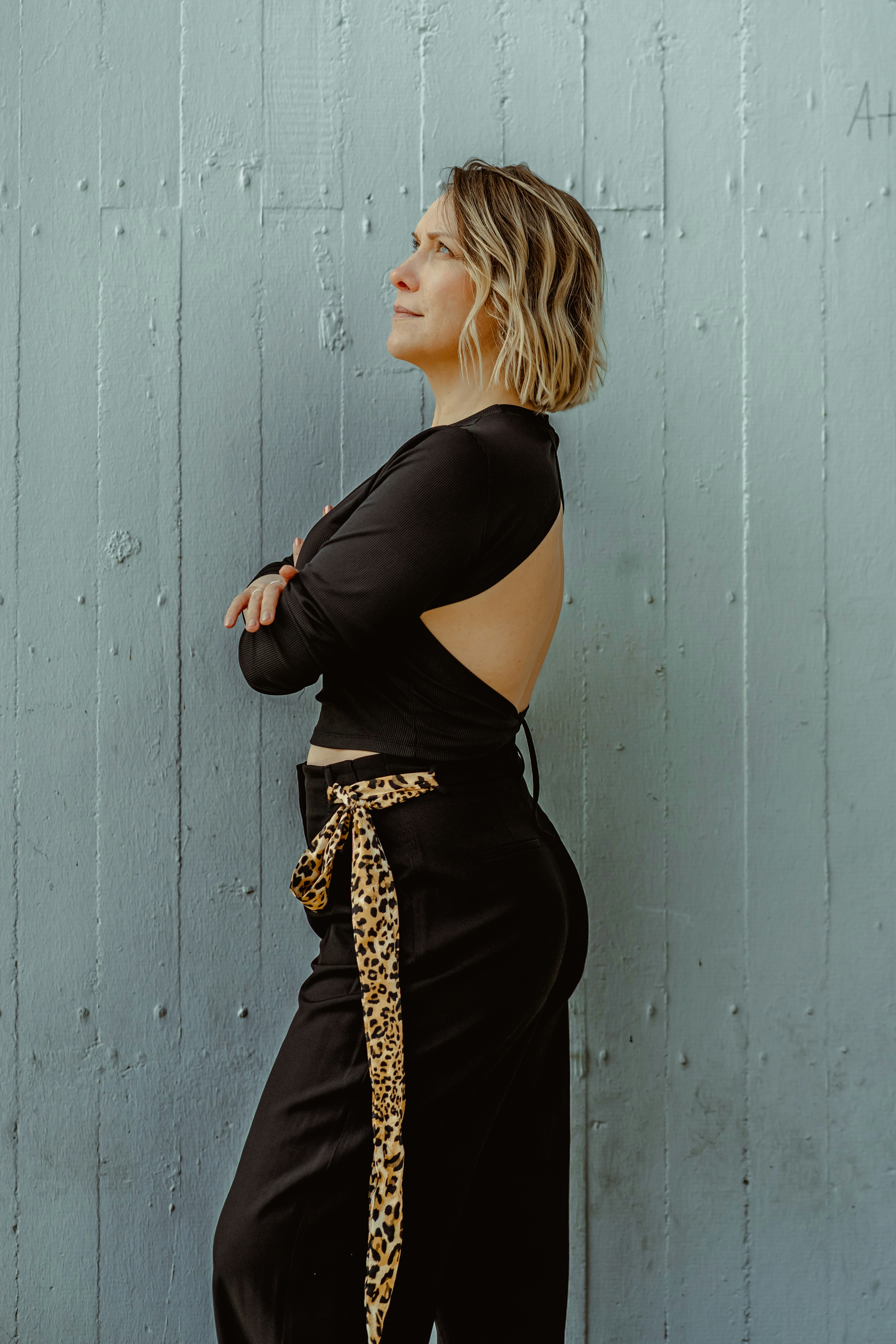 Profile in Light: Woman in Open-Back Dress Stands Against Aged Teal Wall