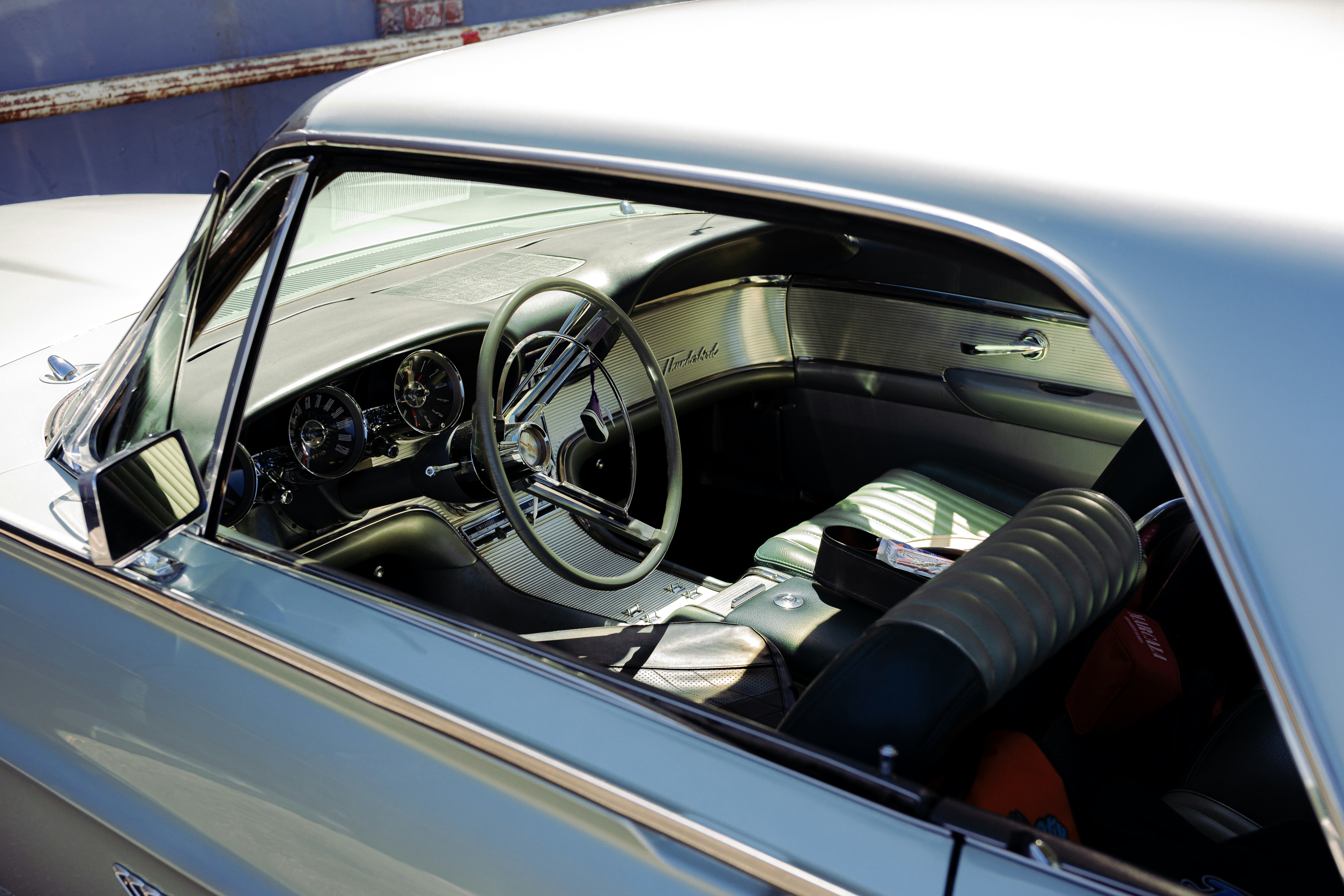 Vintage car dashboard and steering wheel visible through the side window, highlighting chrome instruments and textured upholstery.