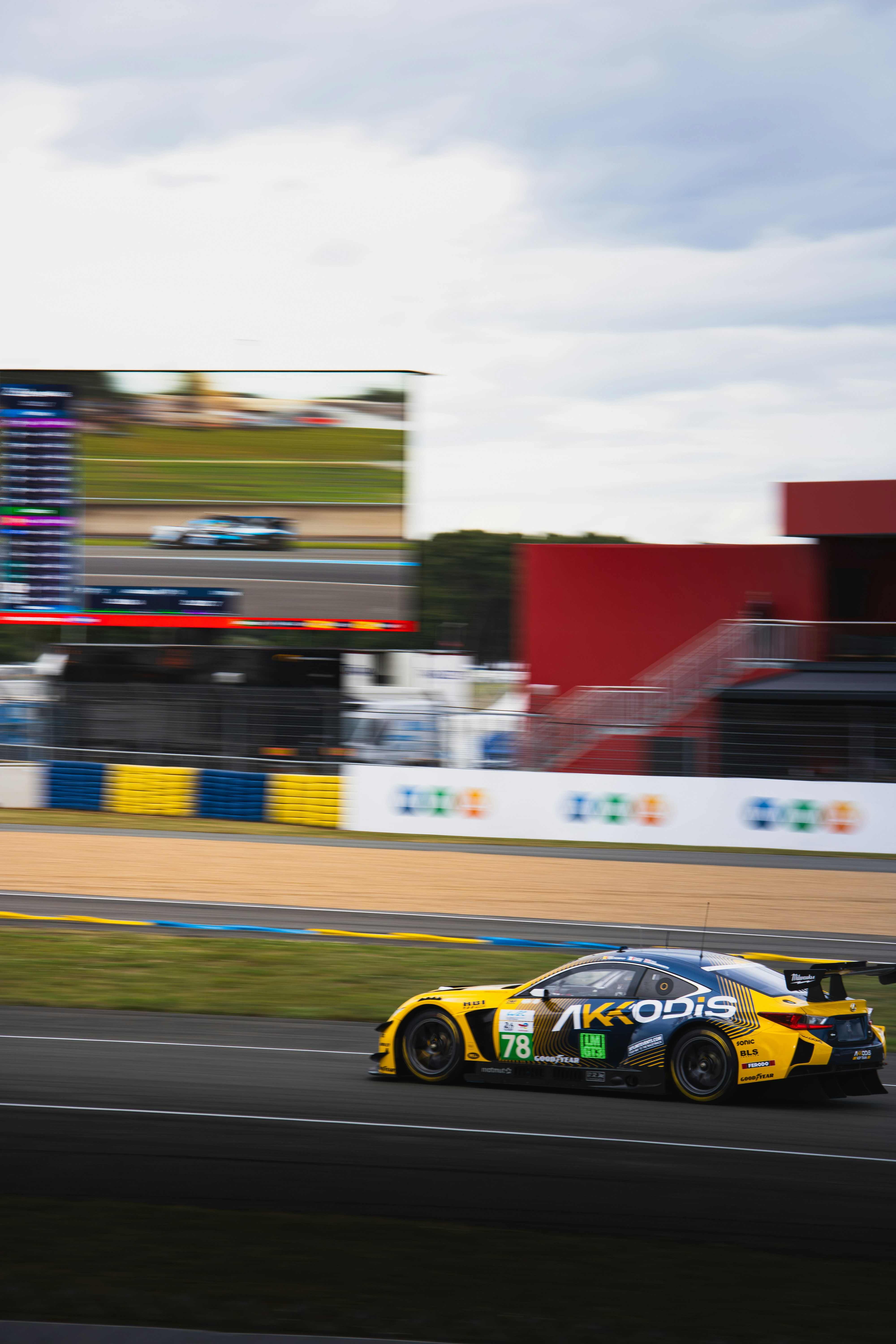 Yellow race car in motion across the track under a blurred grandstand