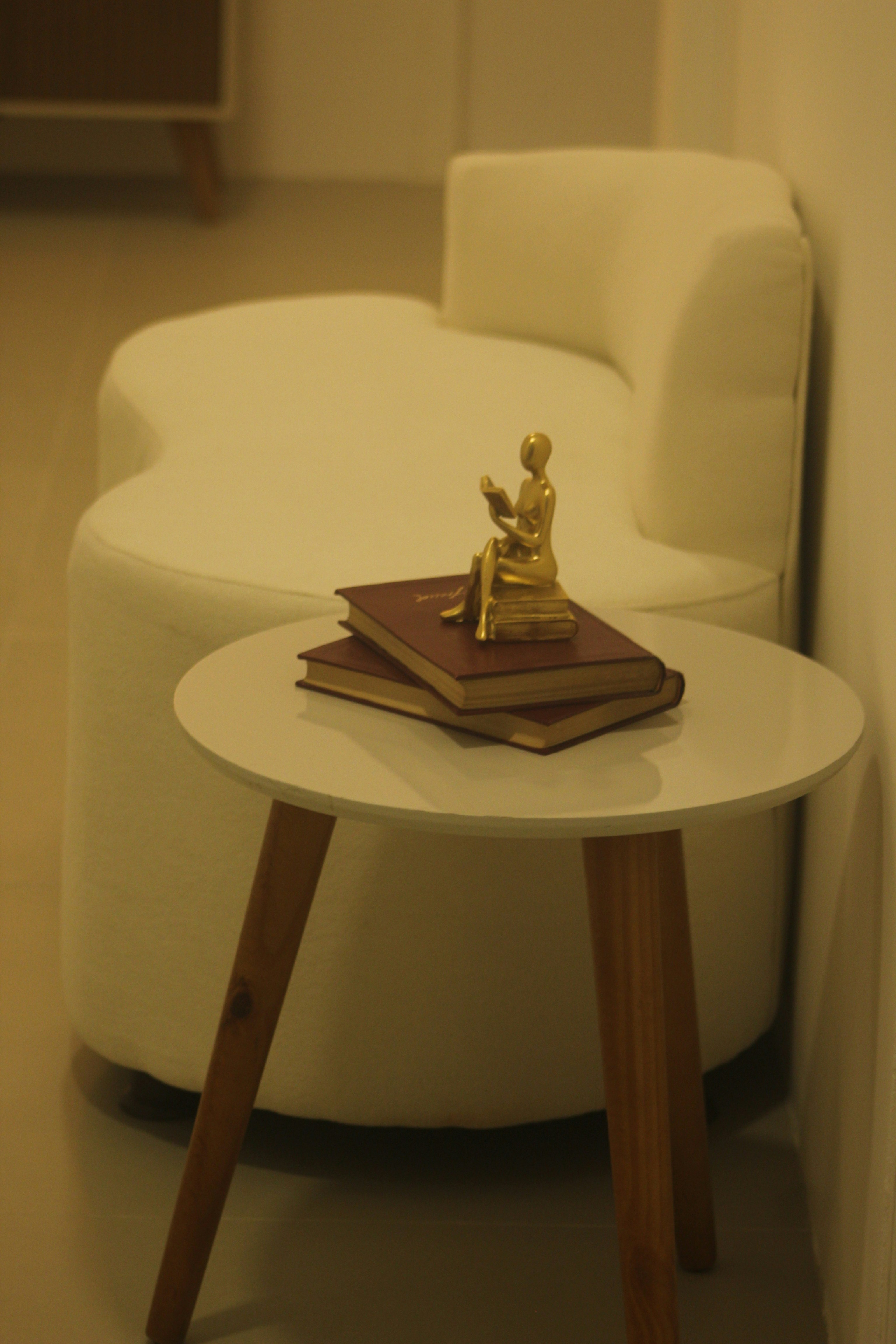 Golden Figurine on a Stack of Books, Nestled Between a Round Table and a White Sofa