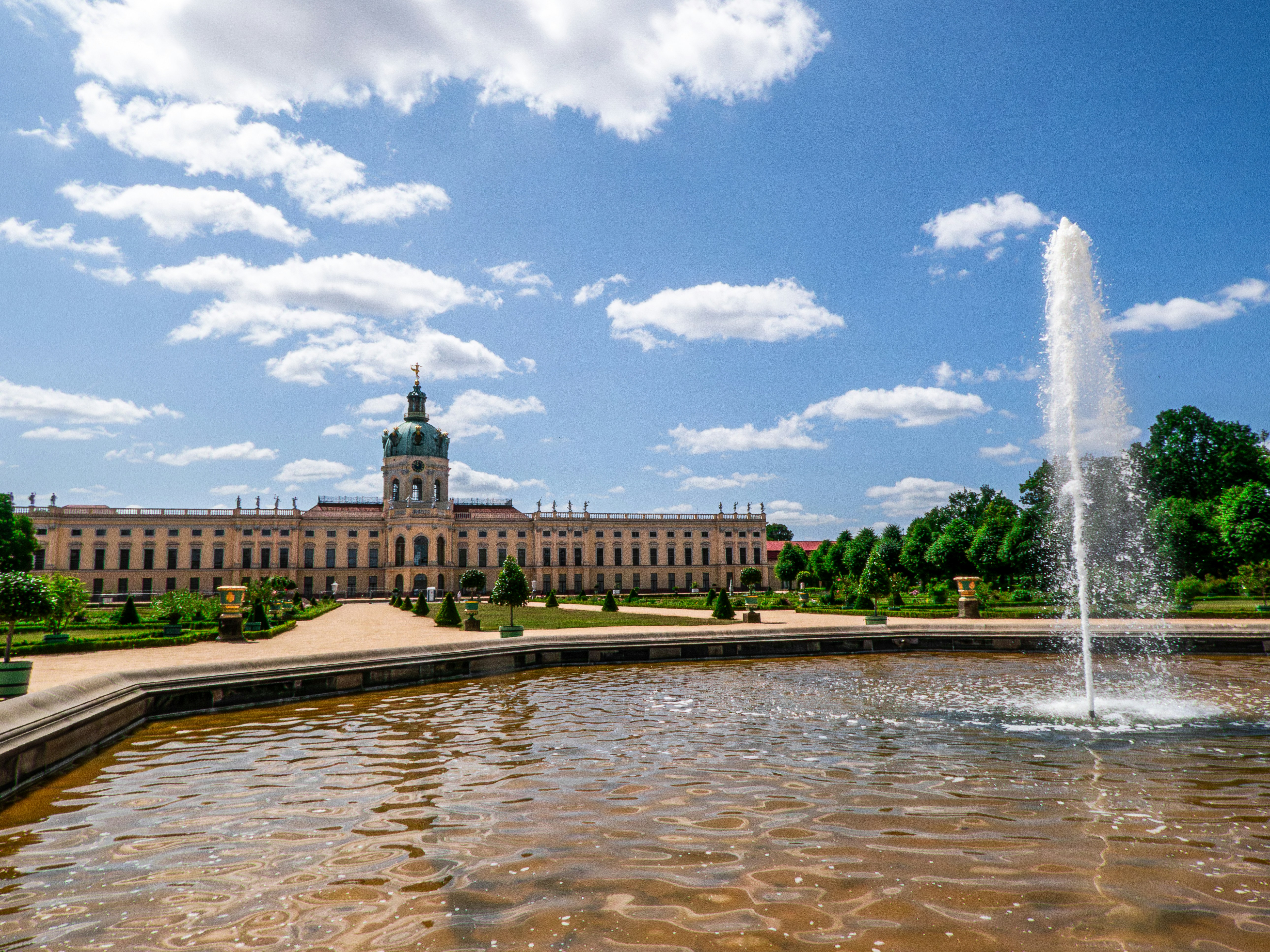 Sunlit Palace Grounds: Fountain, Lagoon, and Baroque Facade