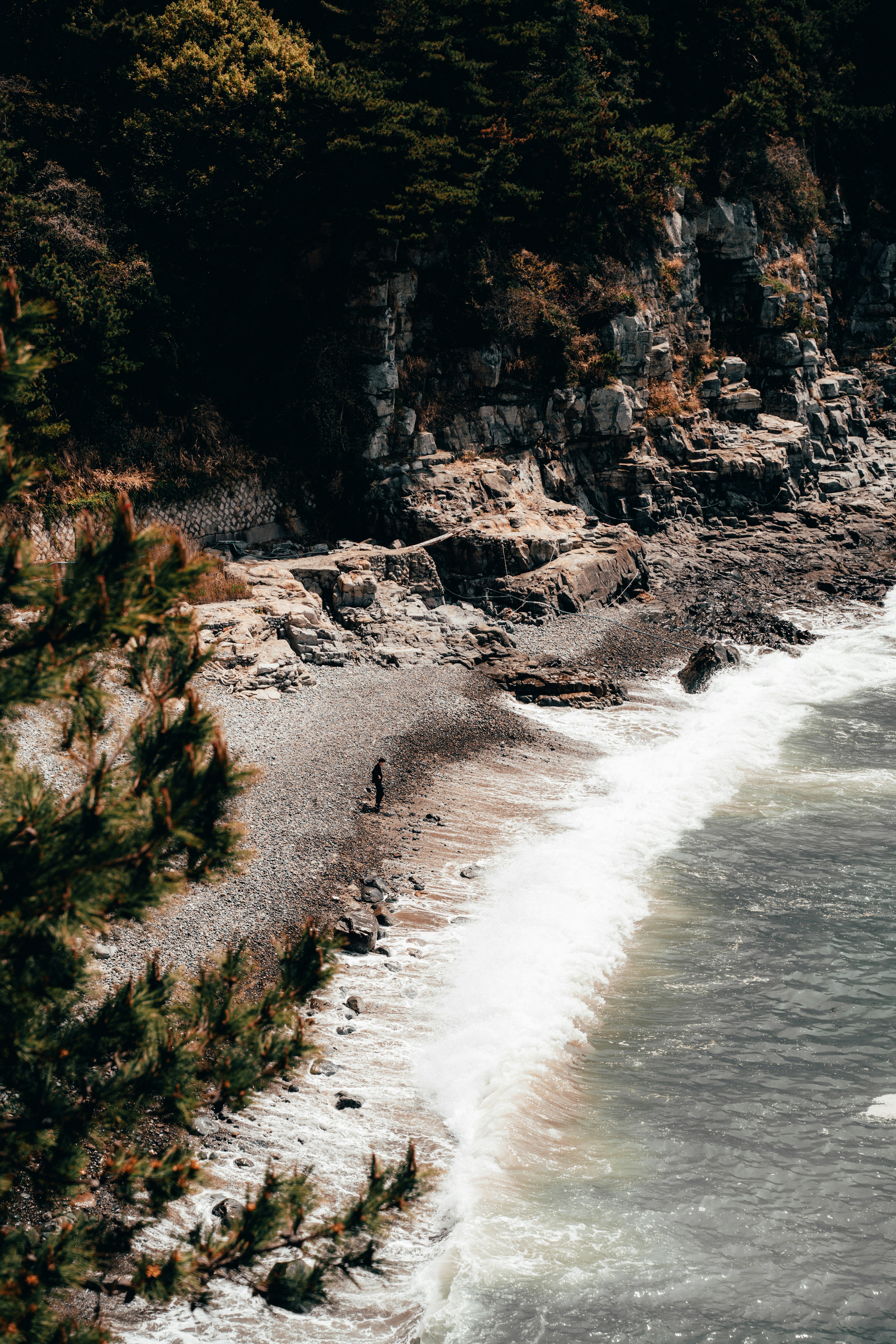 Solitary Figure on a Pebble Strand by Verdant Cliffs