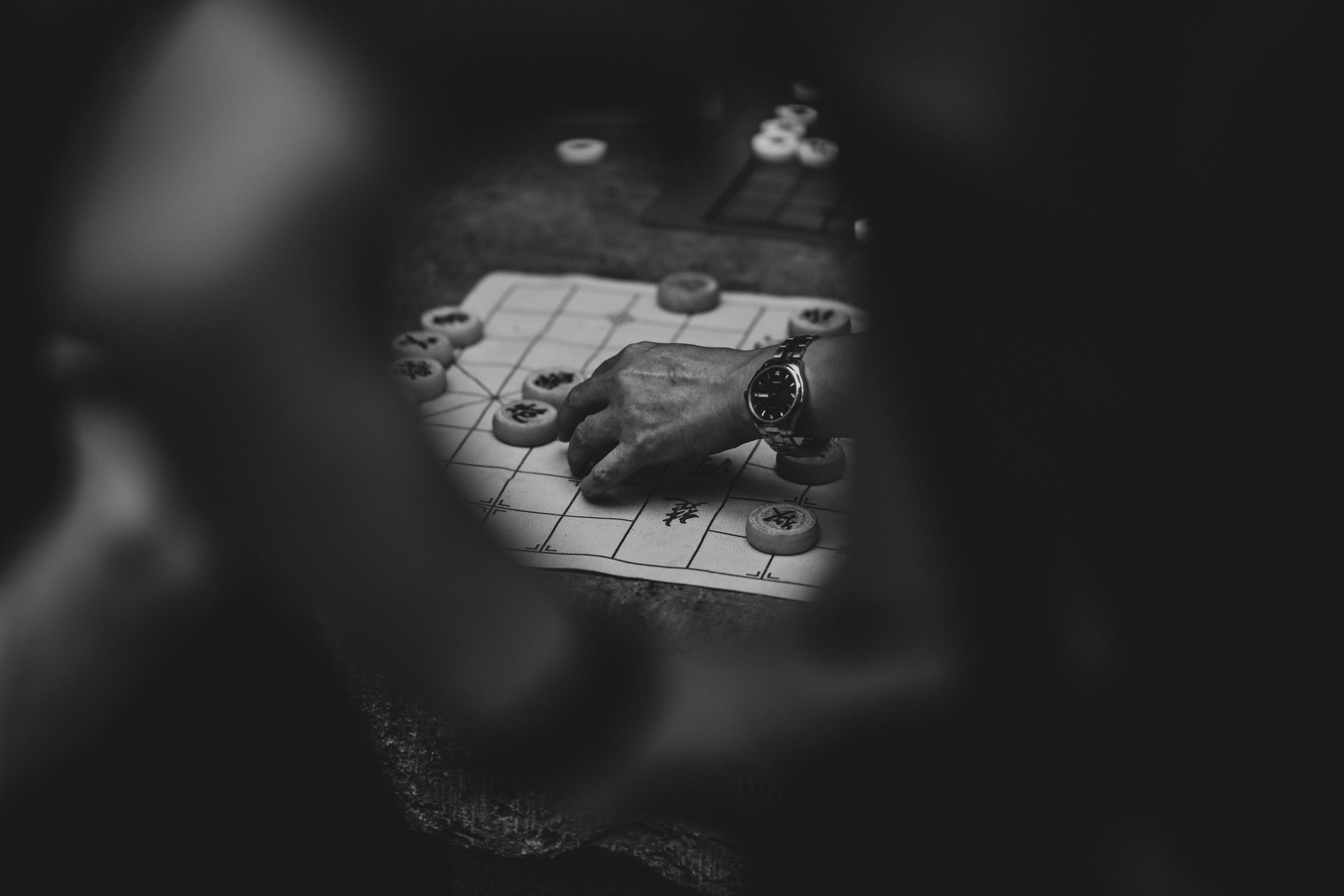 In the Shadowed Circle: A Hand on a Game Board Through a Narrow Aperture