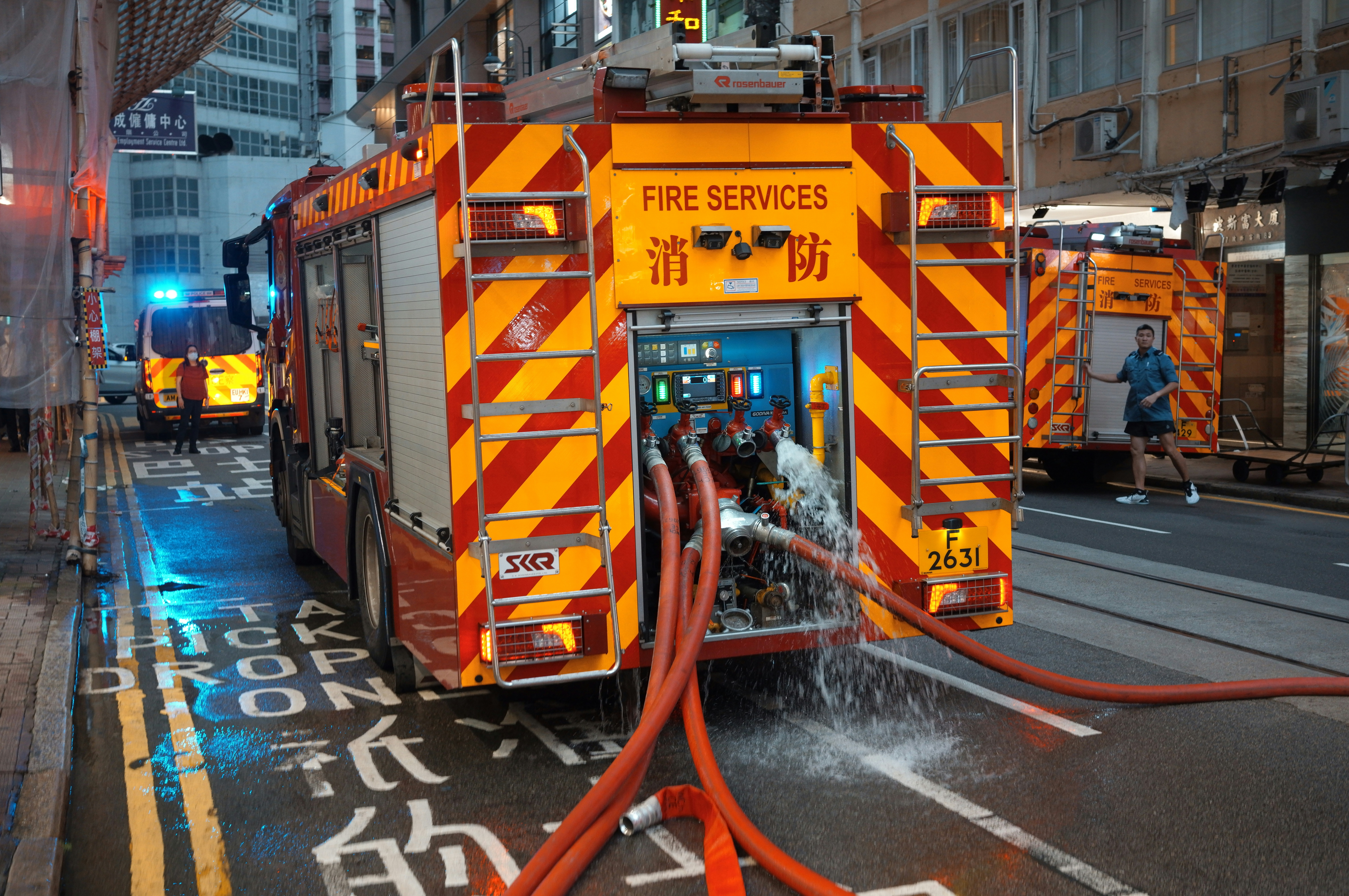 Fire services truck with hoses deployed on a city street; bright reflective markings and open equipment bay suggesting active firefighting operation.
